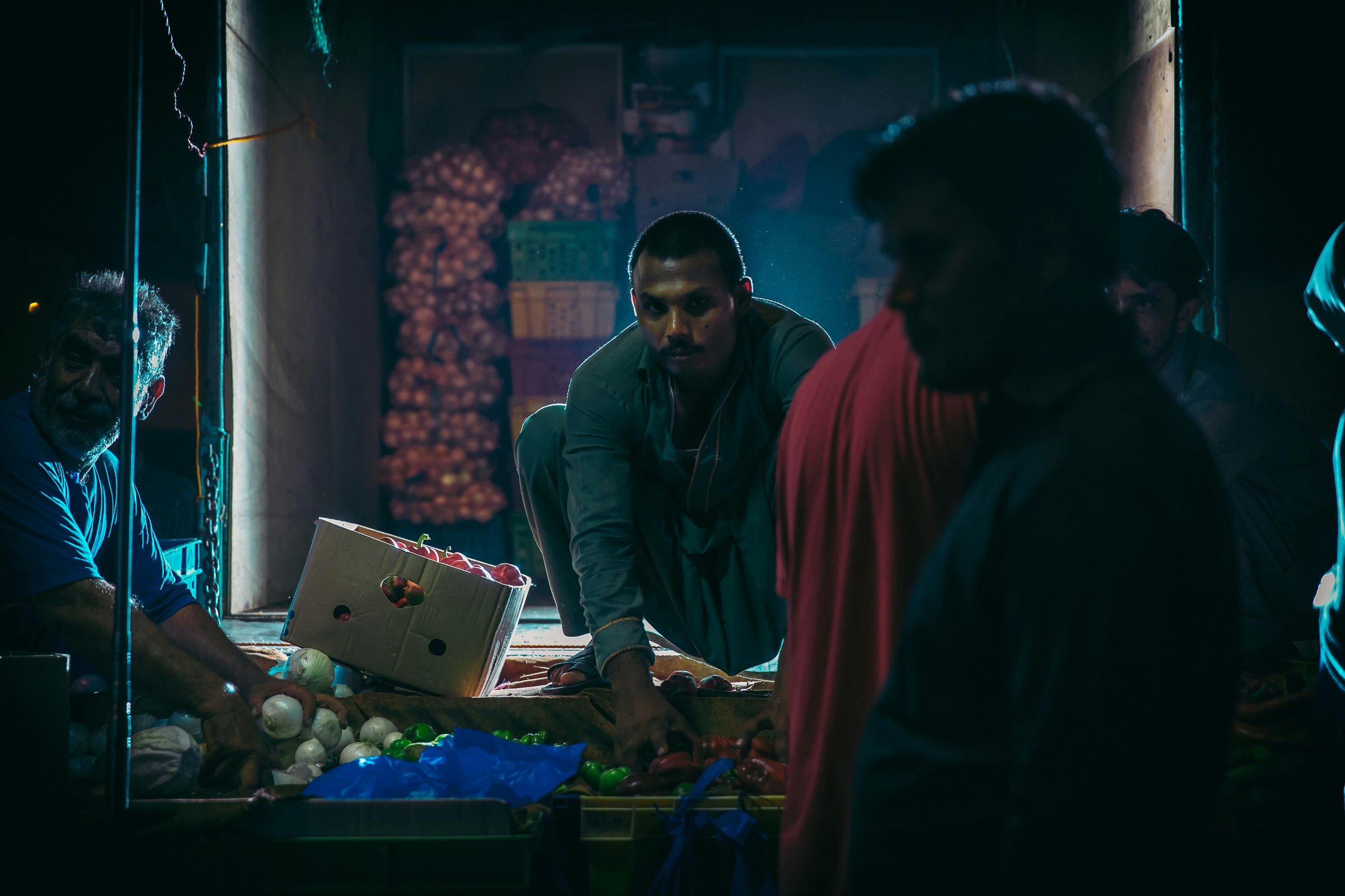 Vendors and customers engage in a bustling night market scene, illuminated by soft light, showcasing a variety of fresh produce.