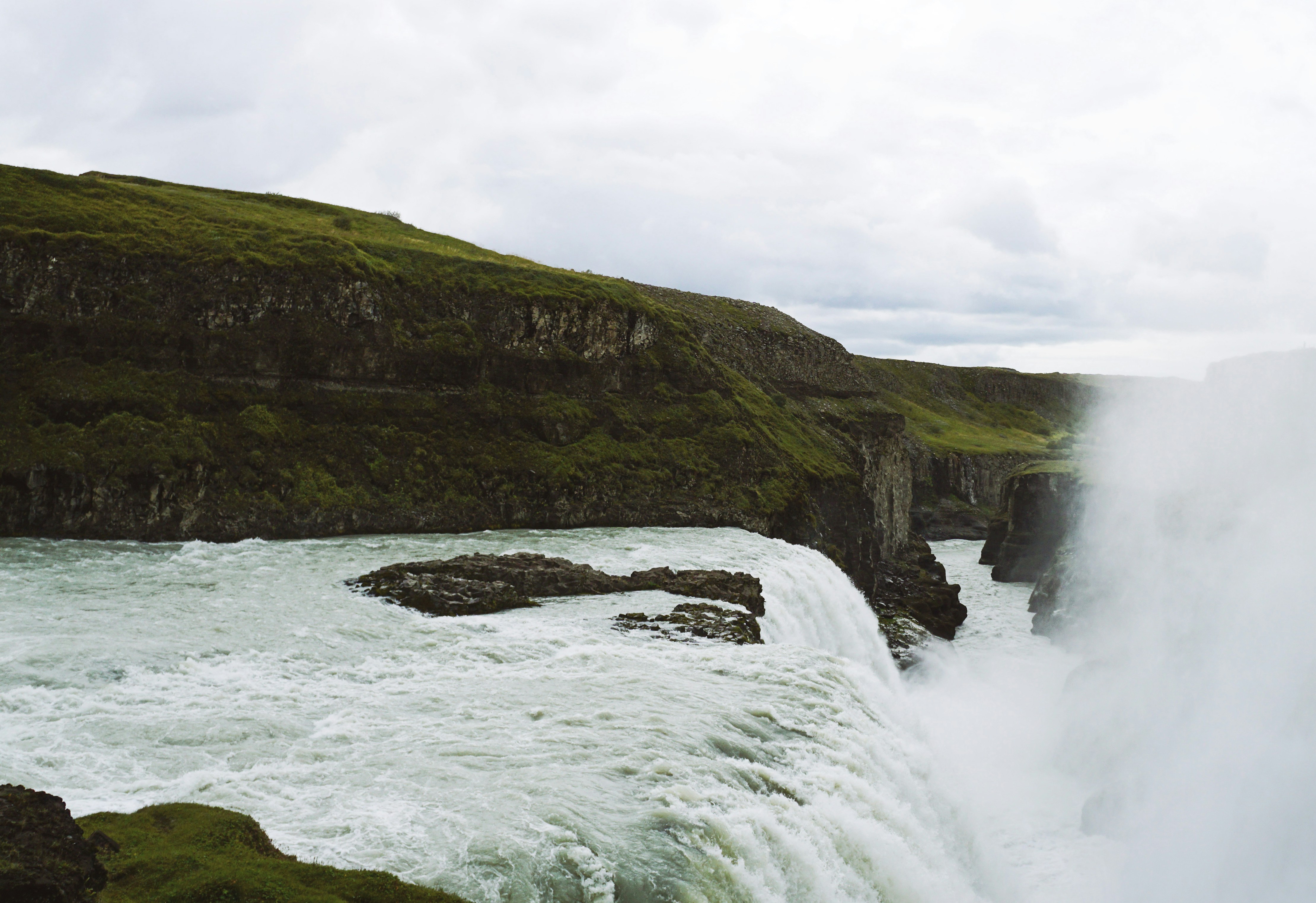 Majestic waterfall plunging into a rocky gorge beneath an overcast sky.