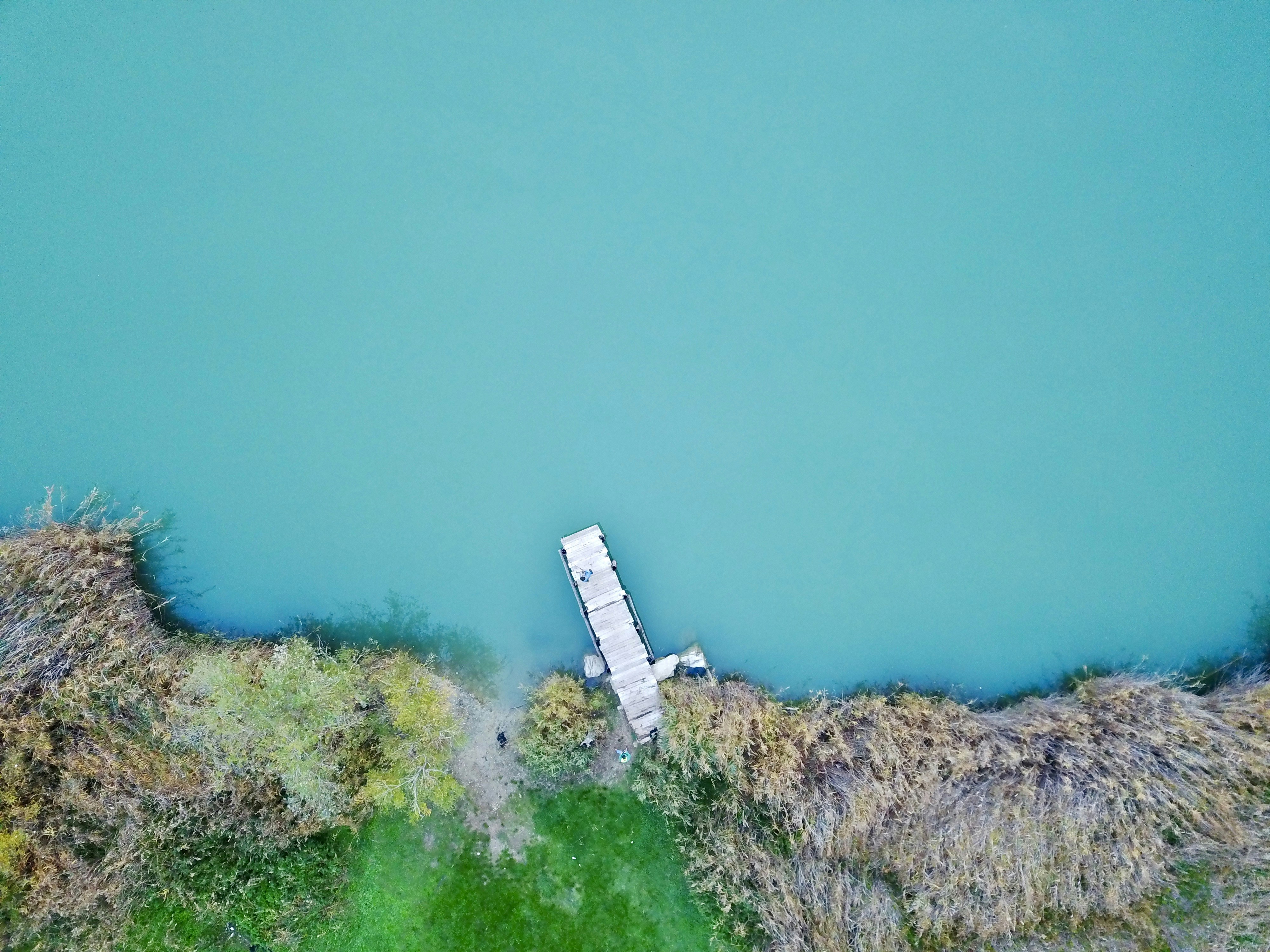White wooden dock extending into tranquil turquoise water surrounded by autumn foliage.