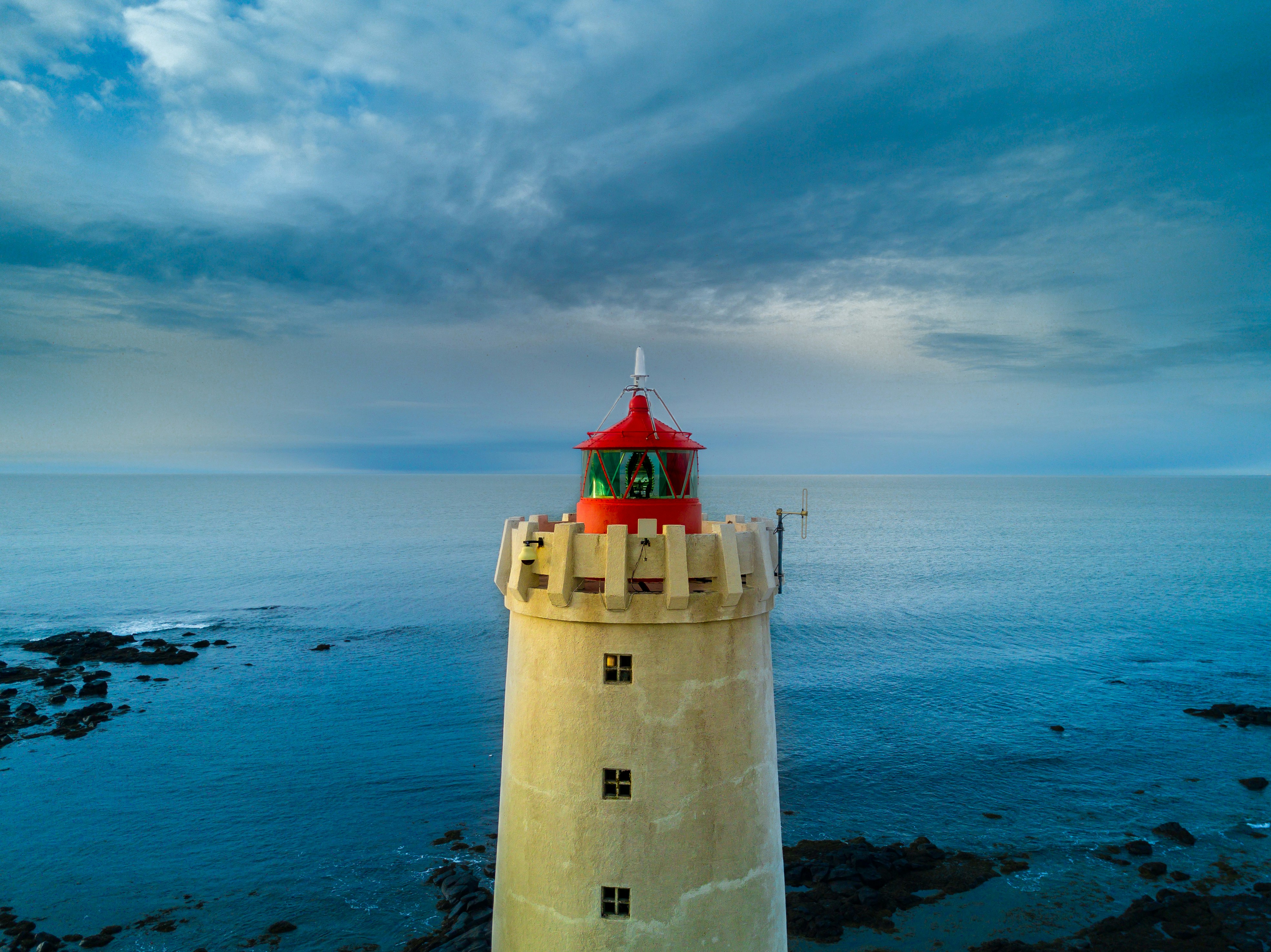 Yellow and red lighthouse standing tall by a serene ocean under a cloudy sky.