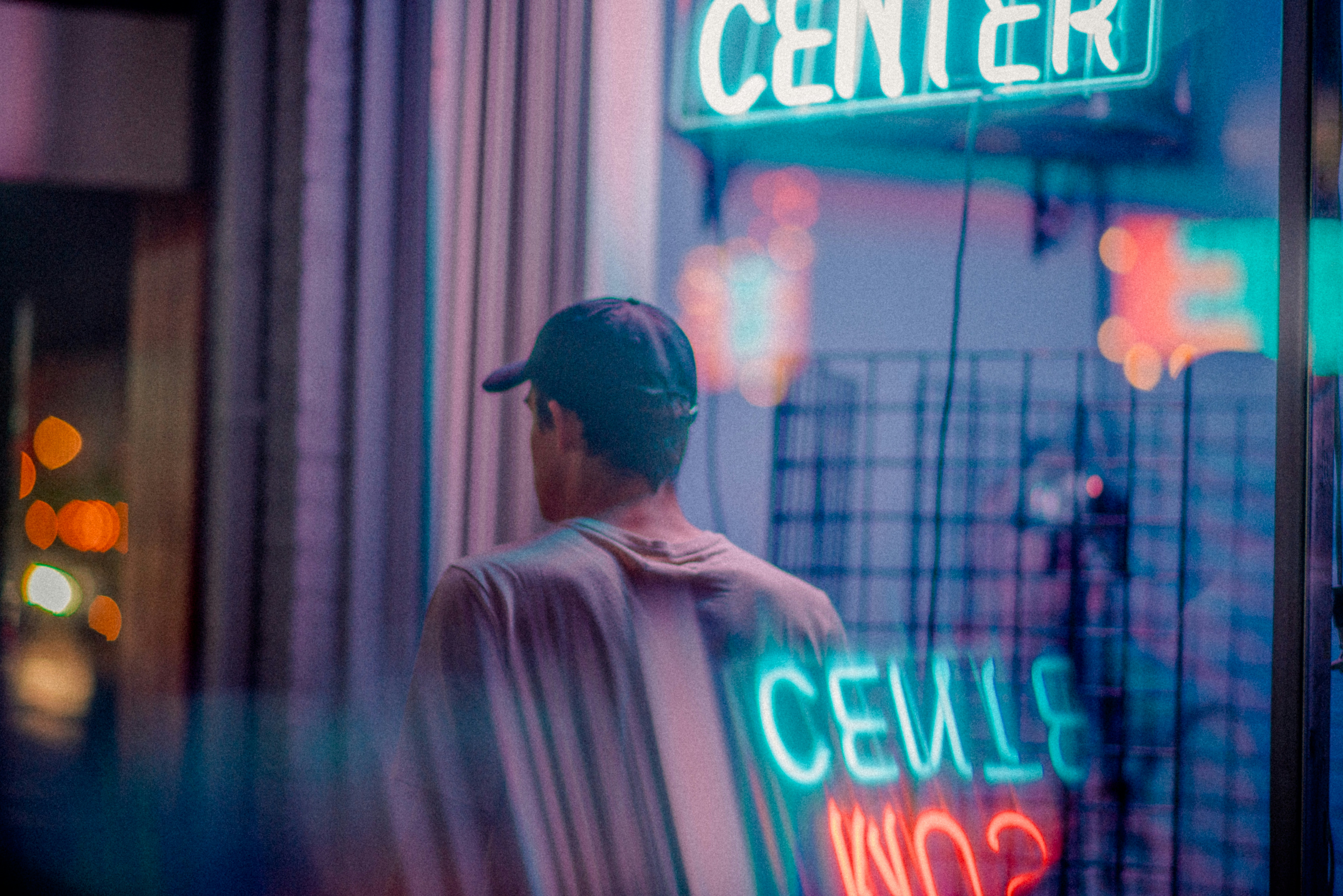 Person walking past vibrant neon signs in an urban setting at night.
