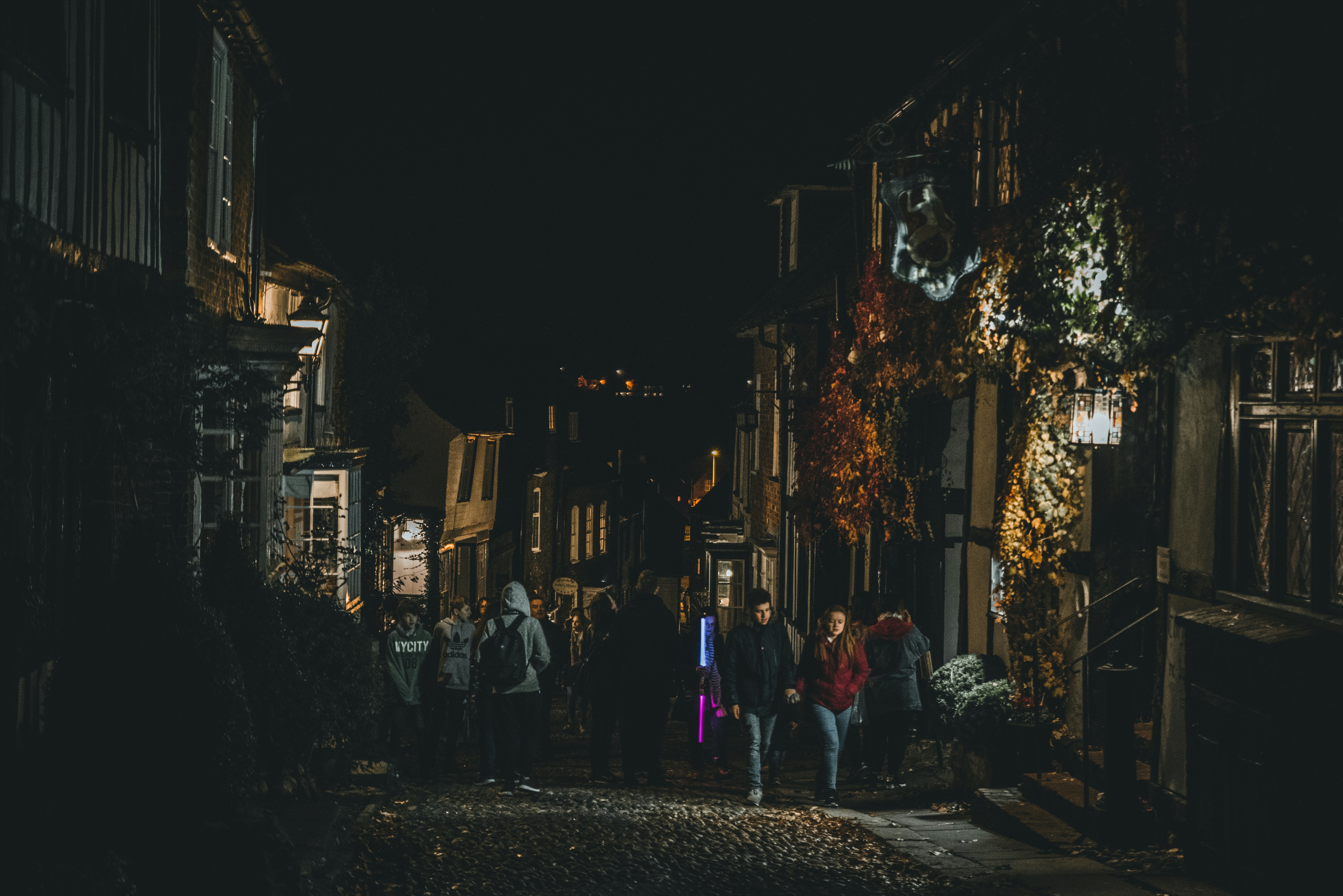 Charming street scene illuminated by soft lights, showcasing people enjoying a night out amid historic architecture and autumn foliage.