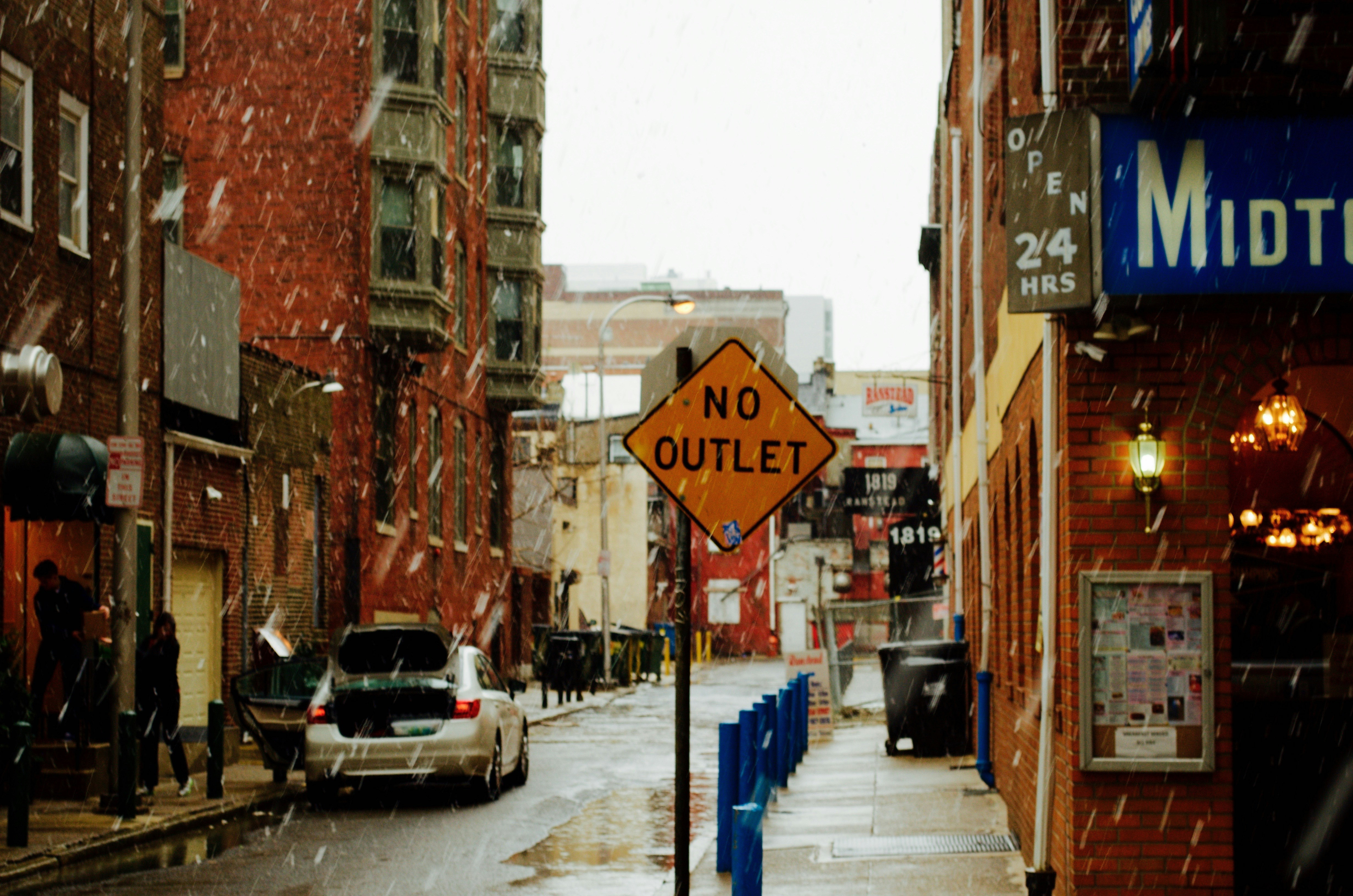 A snow-laden street scene featuring a 'No Outlet' sign amidst a backdrop of brick buildings and falling snowflakes.