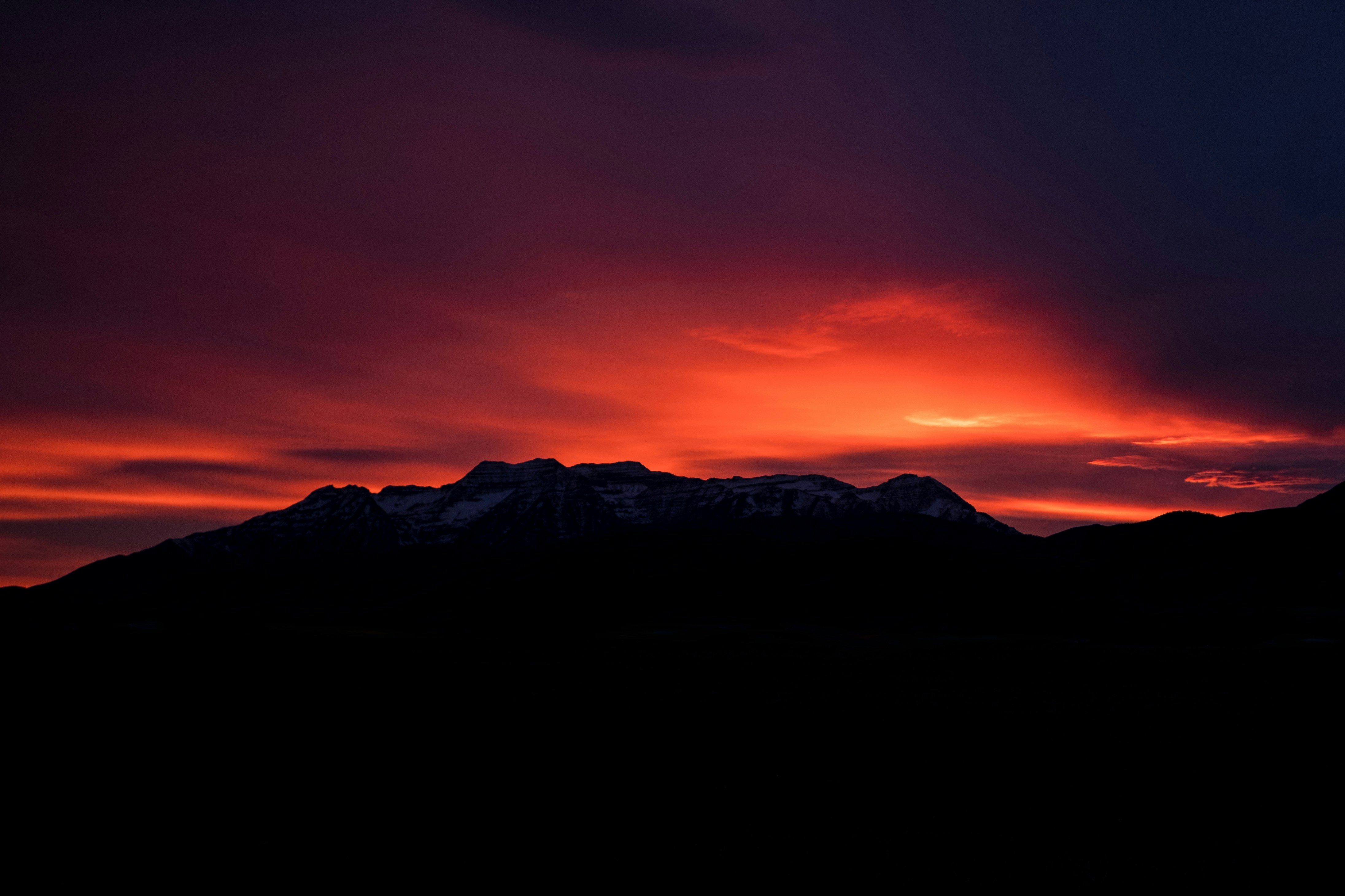 Silhouette of rugged mountains against a vibrant twilight sky, showcasing rich hues of red and purple.