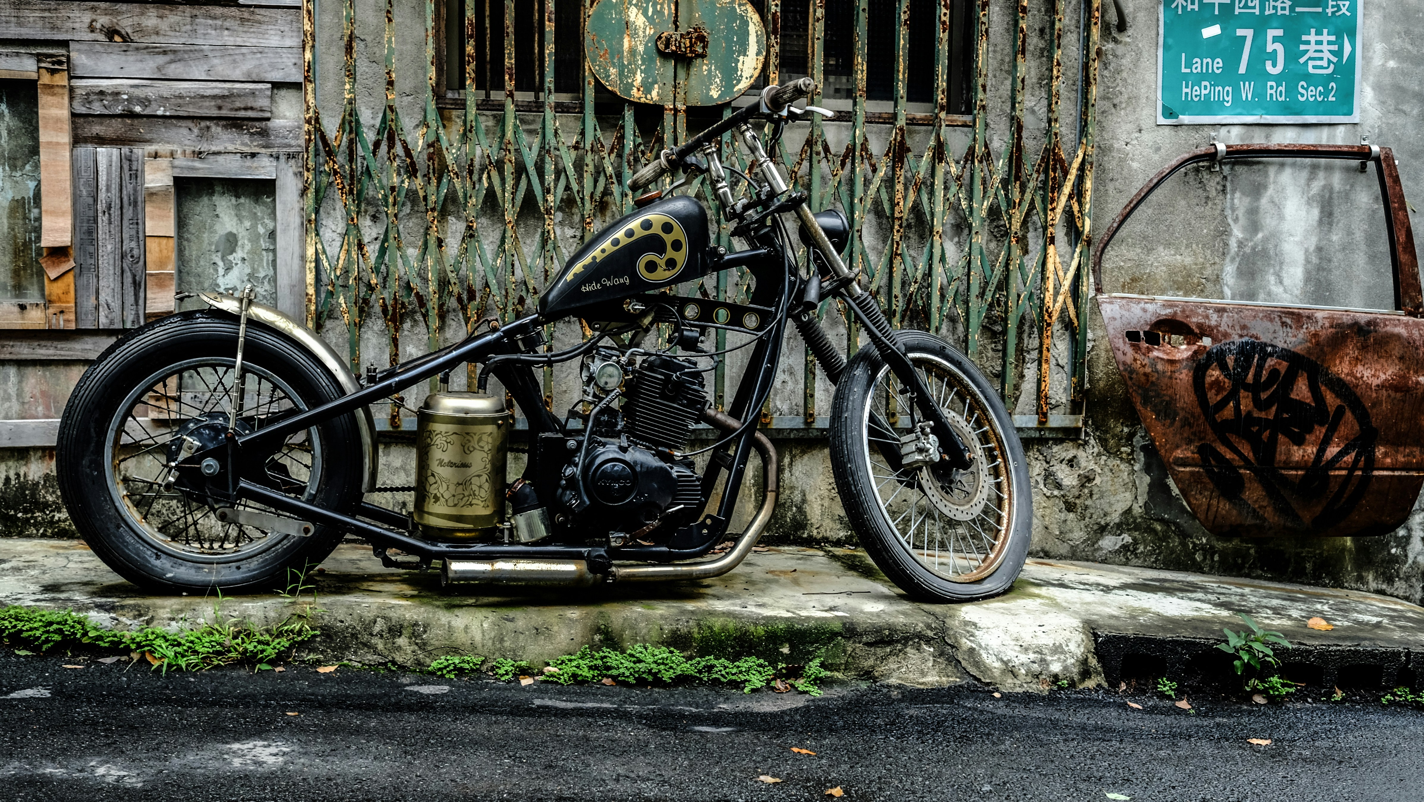 A vintage motorcycle with a unique design rests against a weathered wall, showcasing its intricate details and the passage of time.