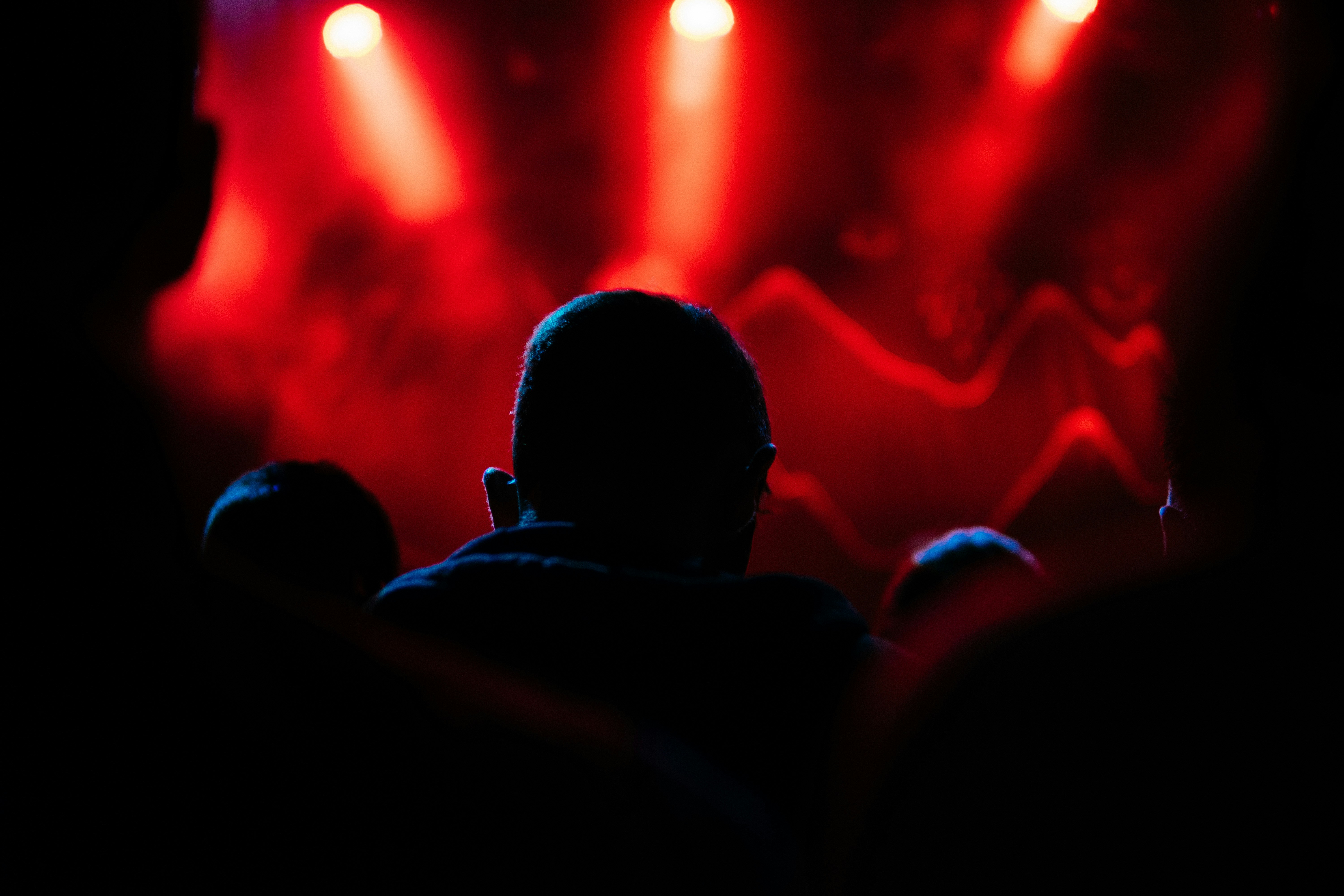 Silhouetted figures in a crowd await the performance, illuminated by vibrant red stage lights.