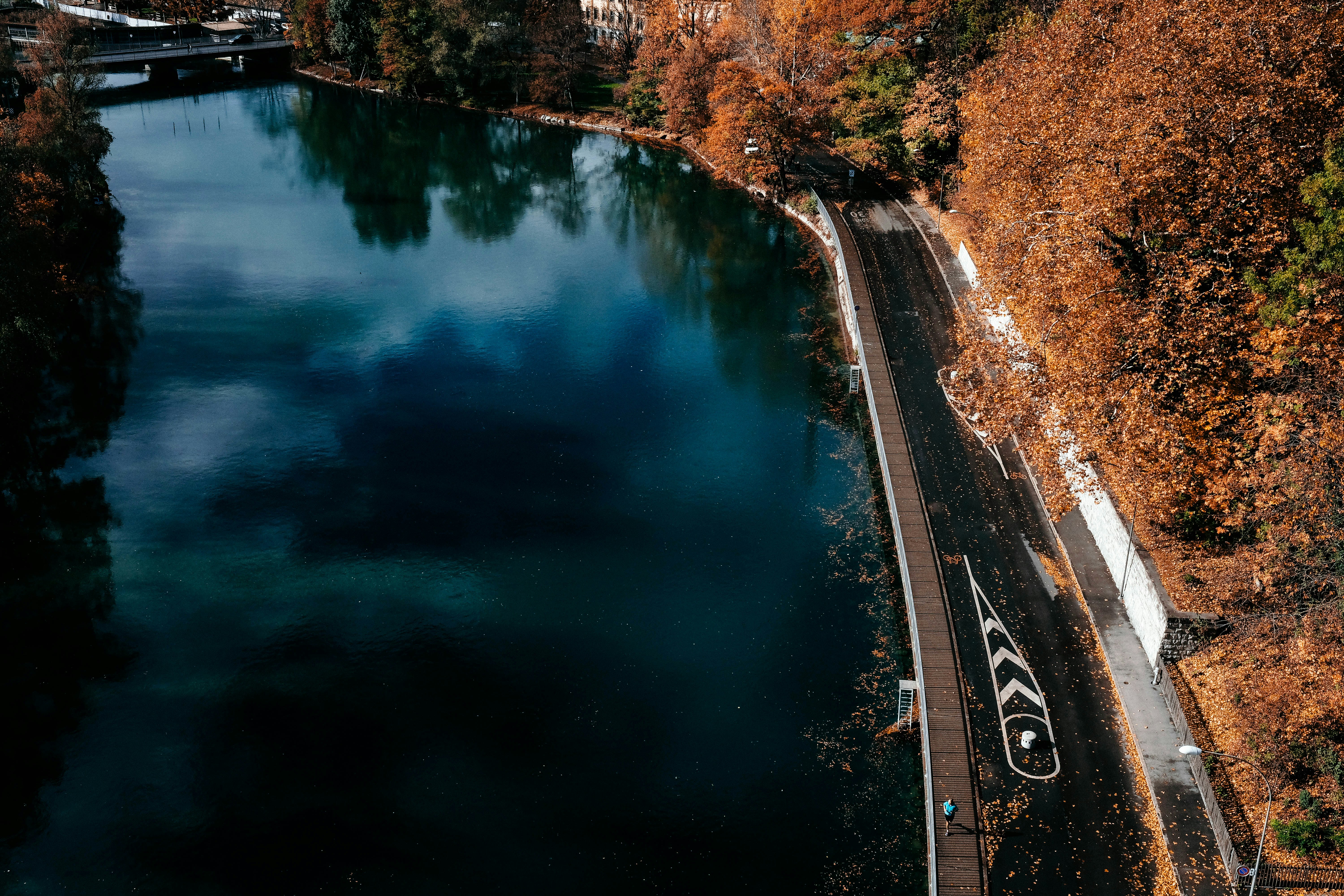 A serene riverside path lined with autumn foliage, reflecting vibrant colors on the calm water surface. The scene invites peaceful contemplation.