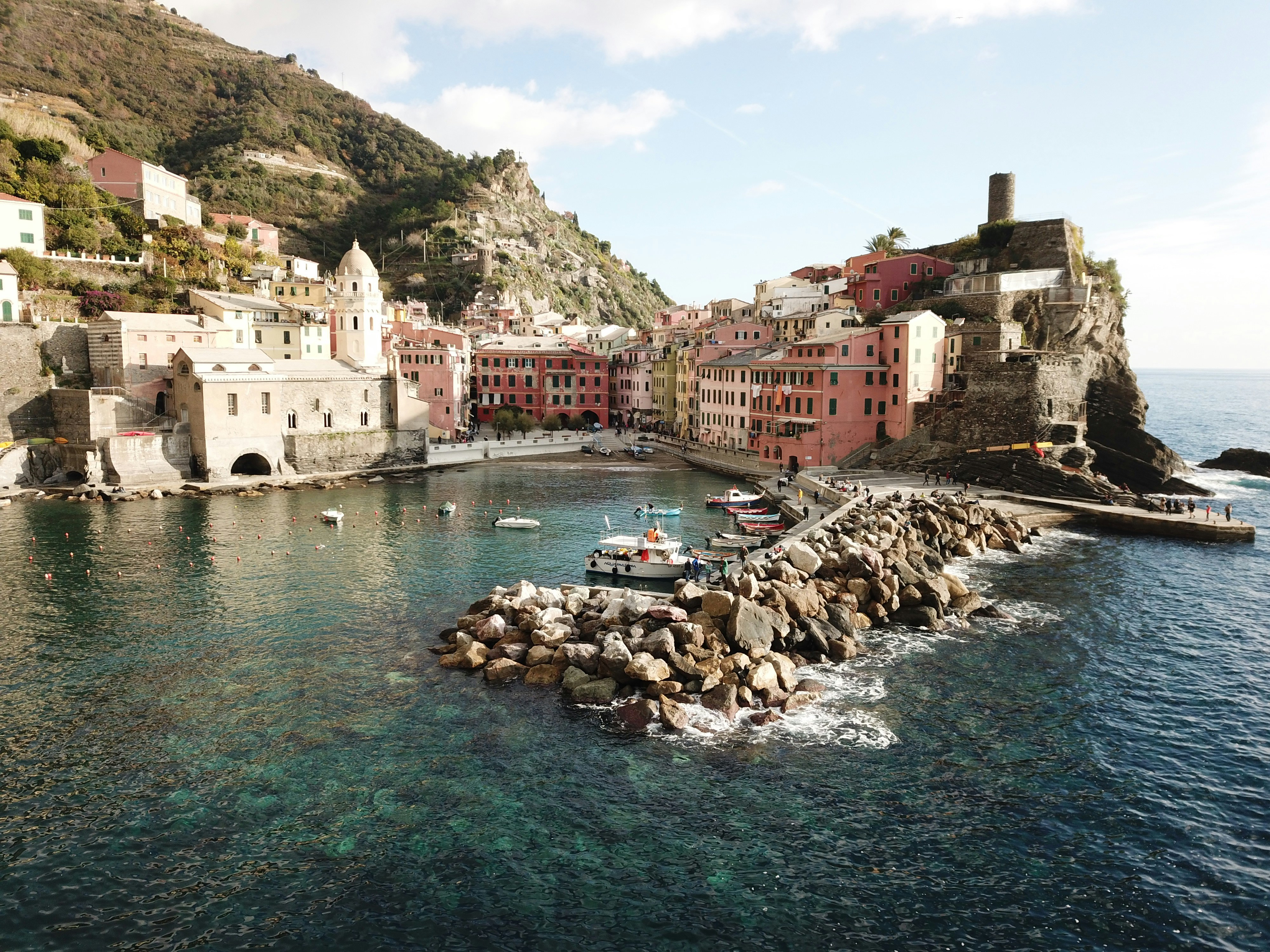 Colorful seaside village with boats docked in a tranquil harbor, surrounded by rugged cliffs and clear blue water.