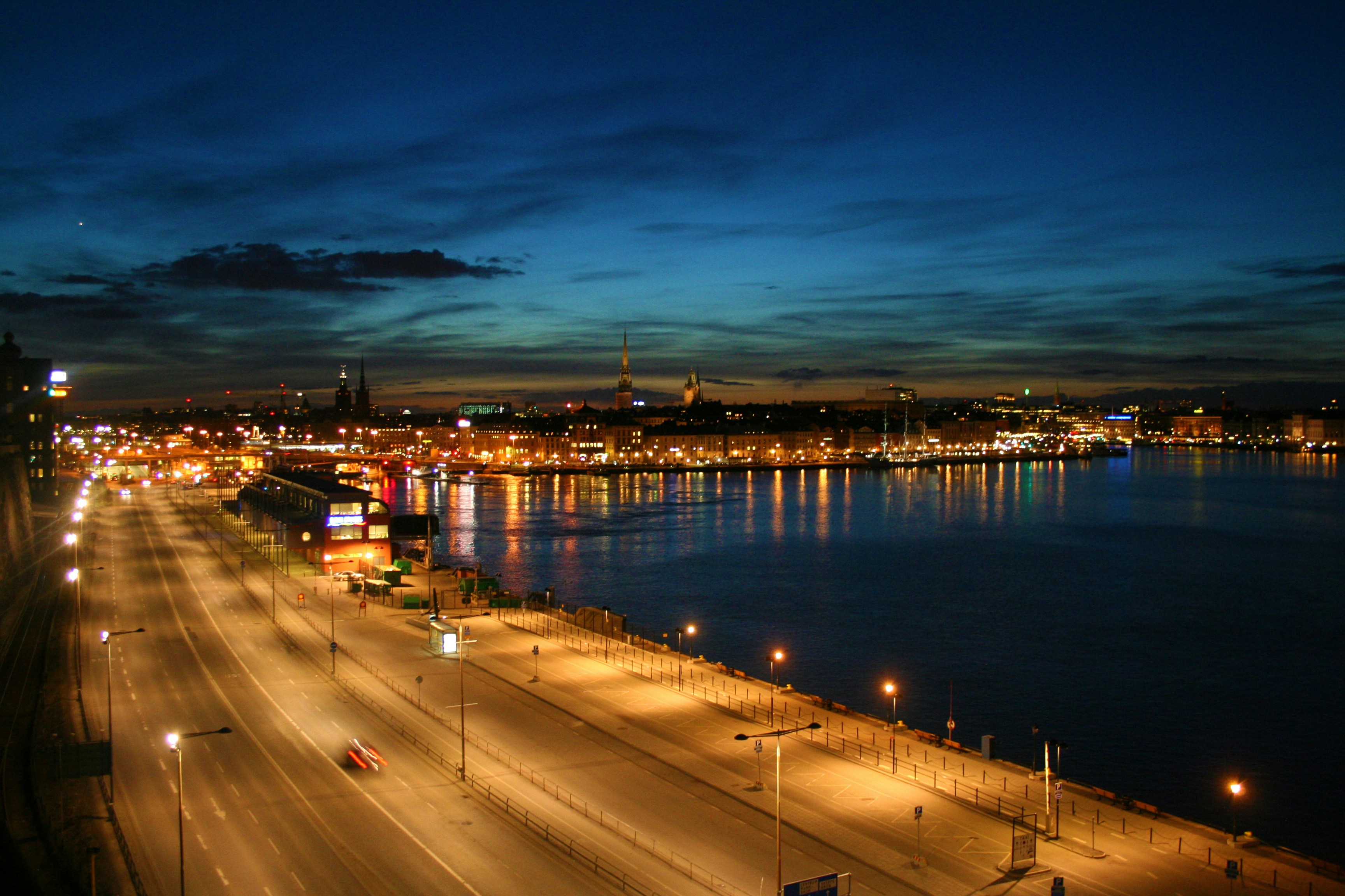 City lights reflecting on the serene waters at dusk, with a vibrant skyline under a deep blue sky.
