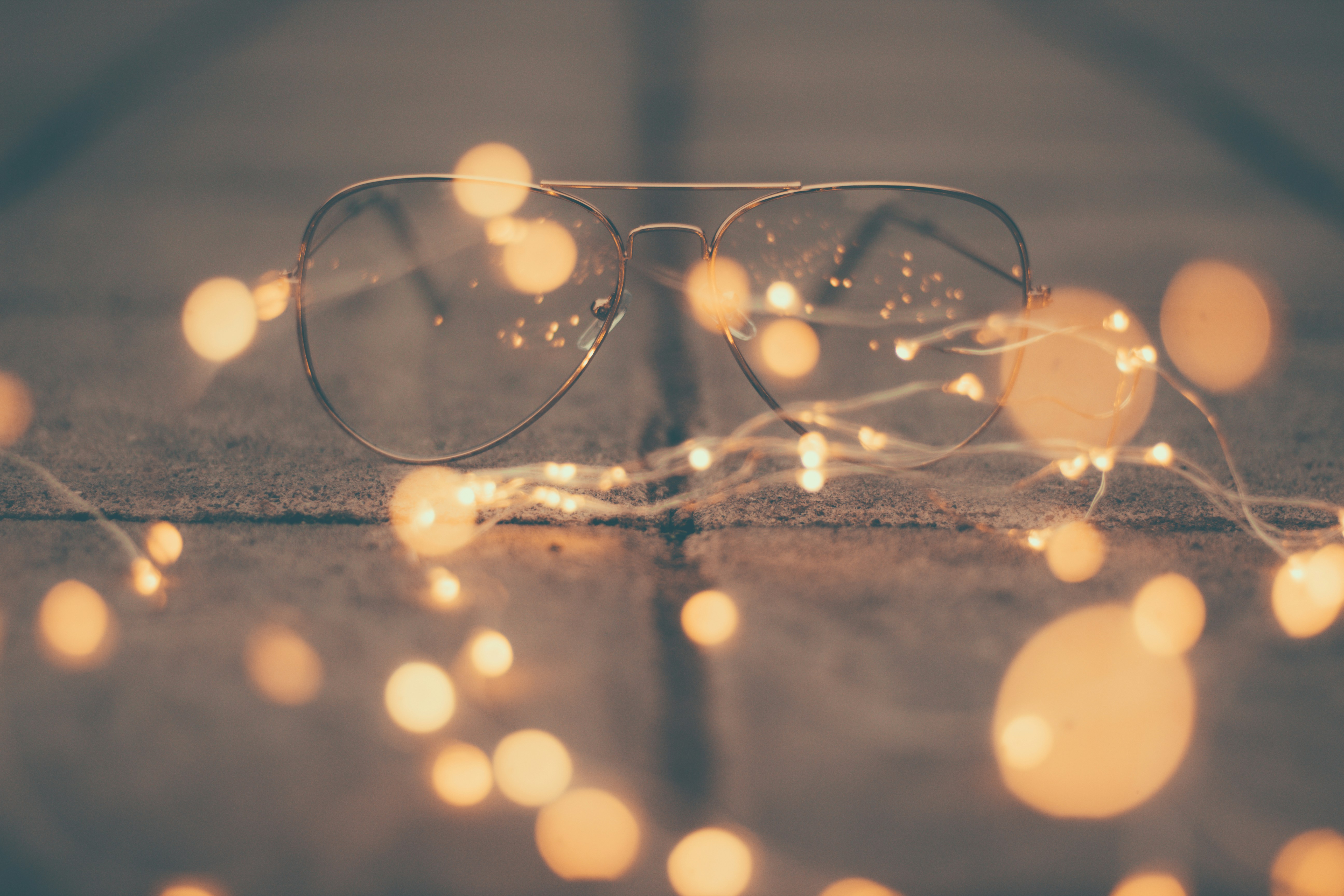 Aviator sunglasses on a surface surrounded by warm bokeh lights.