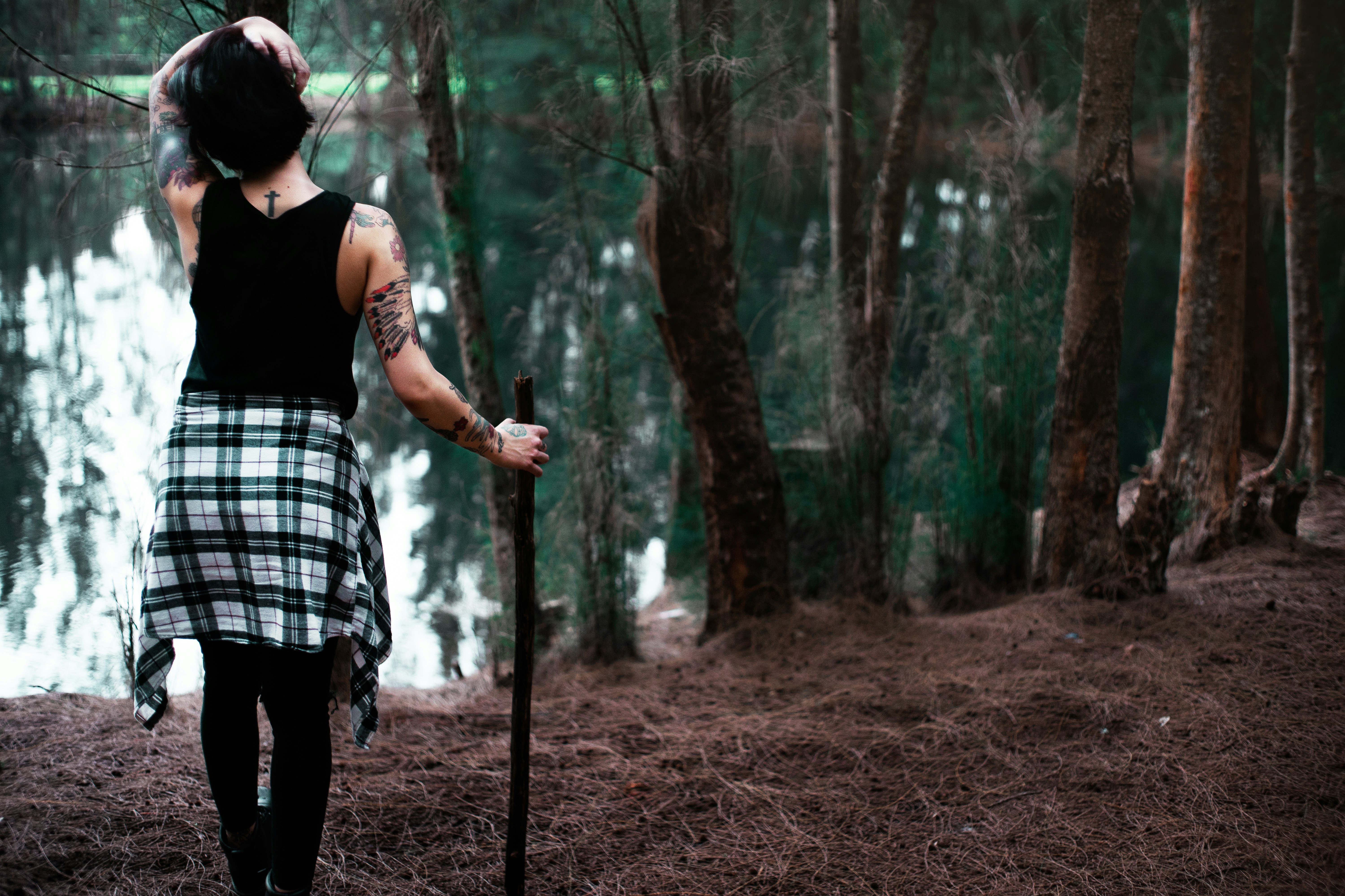 Edge of Quiet Water: A lone figure with a staff along a pine-needle shoreline