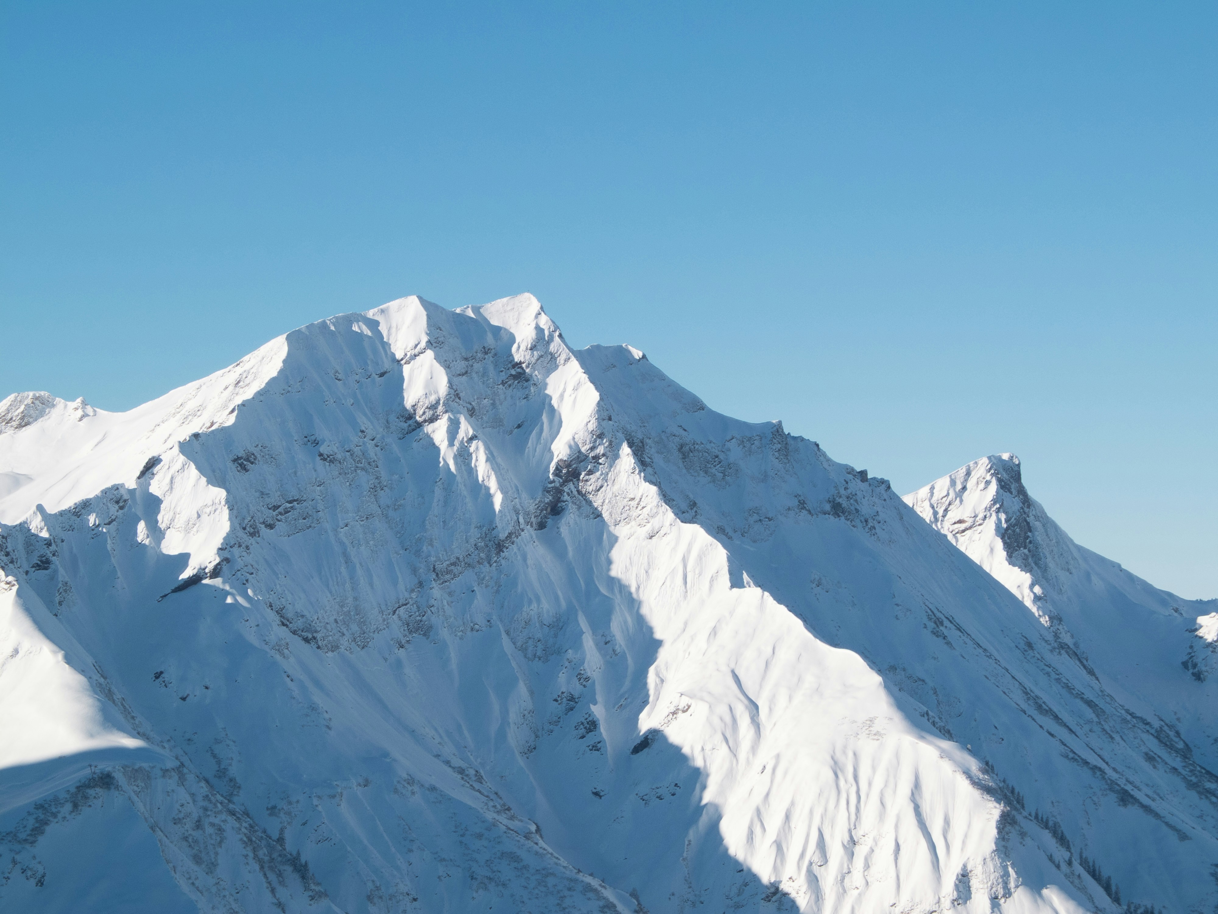 Snow-covered mountain range under a clear blue sky, showcasing the rugged beauty of alpine terrain.