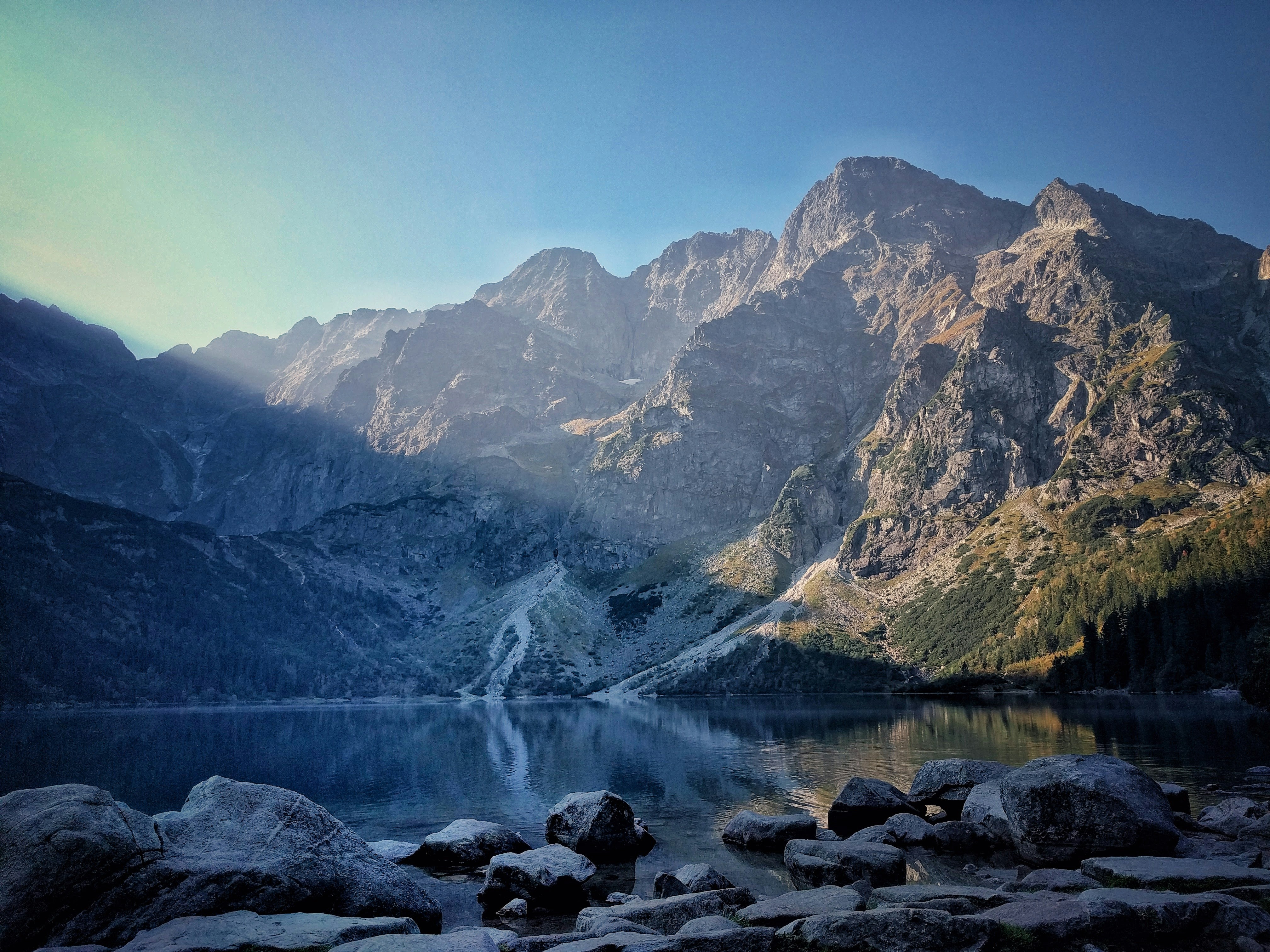 Sunlight streams over rugged mountains reflecting in a tranquil lake.