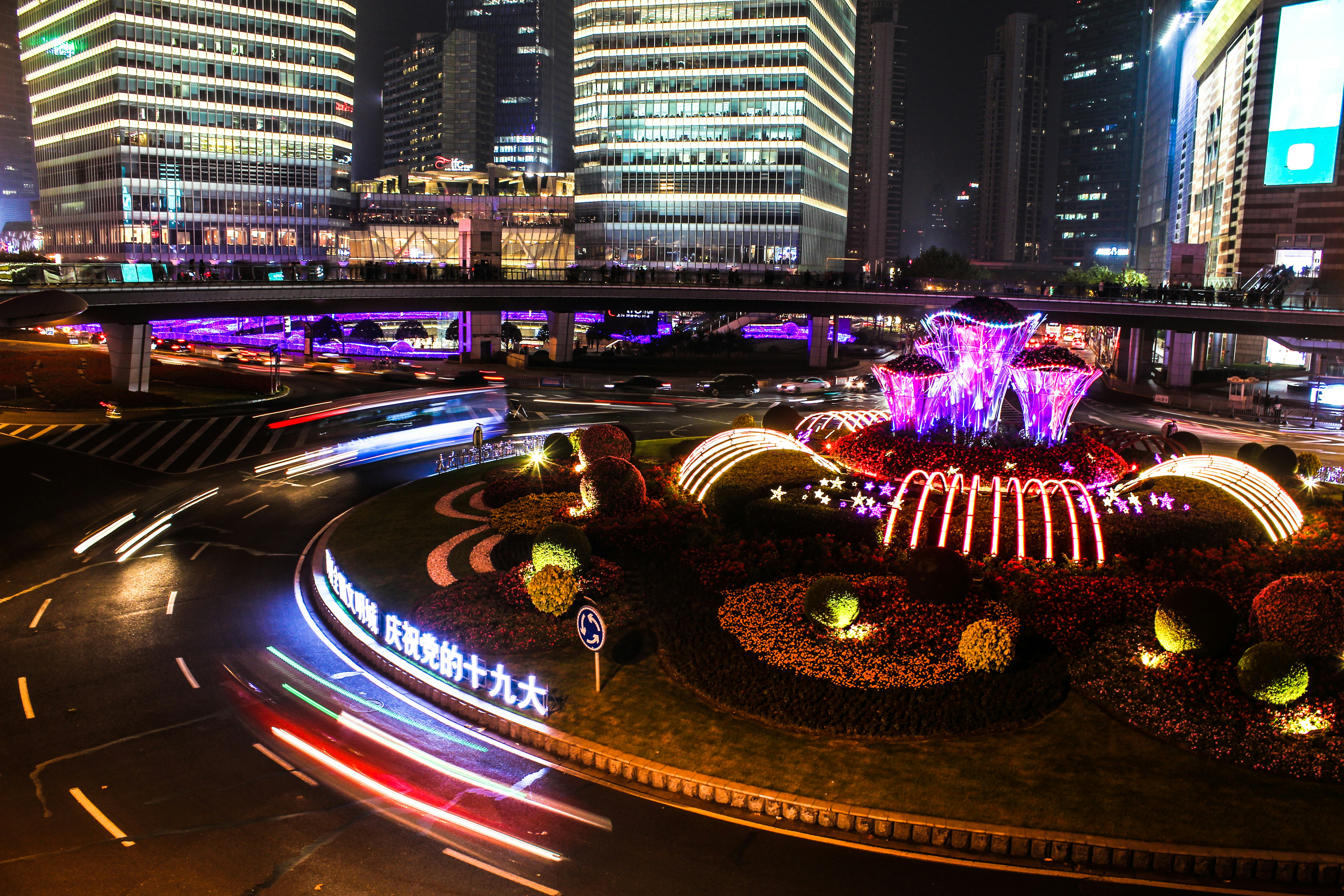 Colorful light trails encircle a vibrant roundabout in Lujiazui at night, framed by towering skyscrapers.