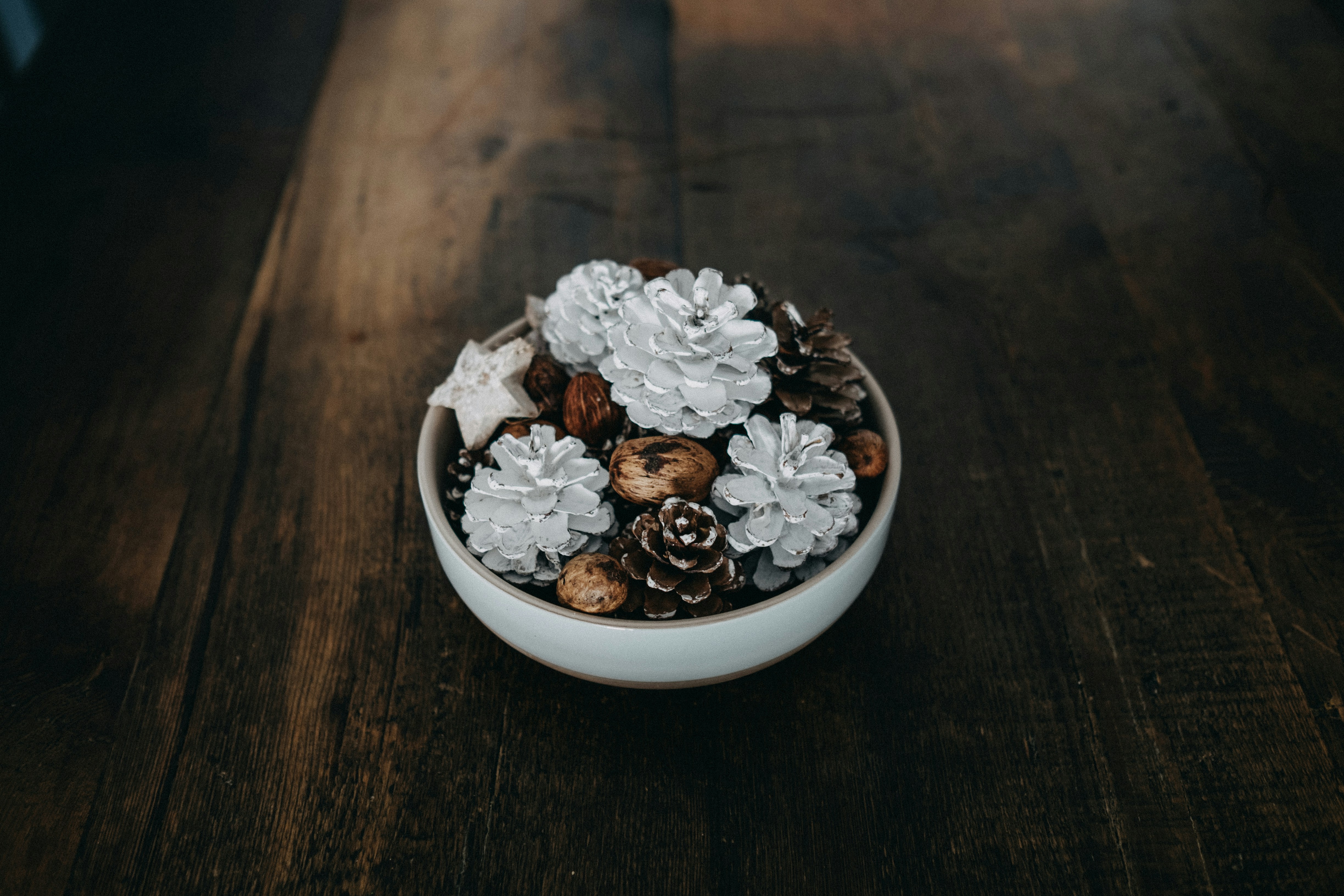 A decorative bowl filled with white-painted pinecones and natural elements resting on a wooden surface.
