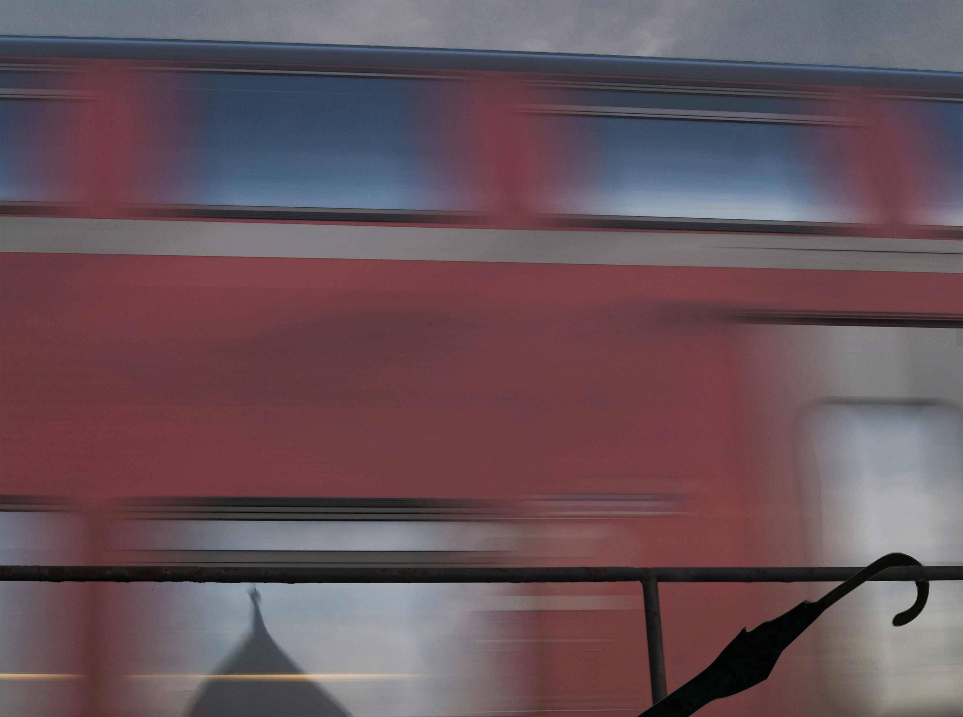 A blurred train rushes past, contrasting with a stationary umbrella and the silhouette of a tower in the background.