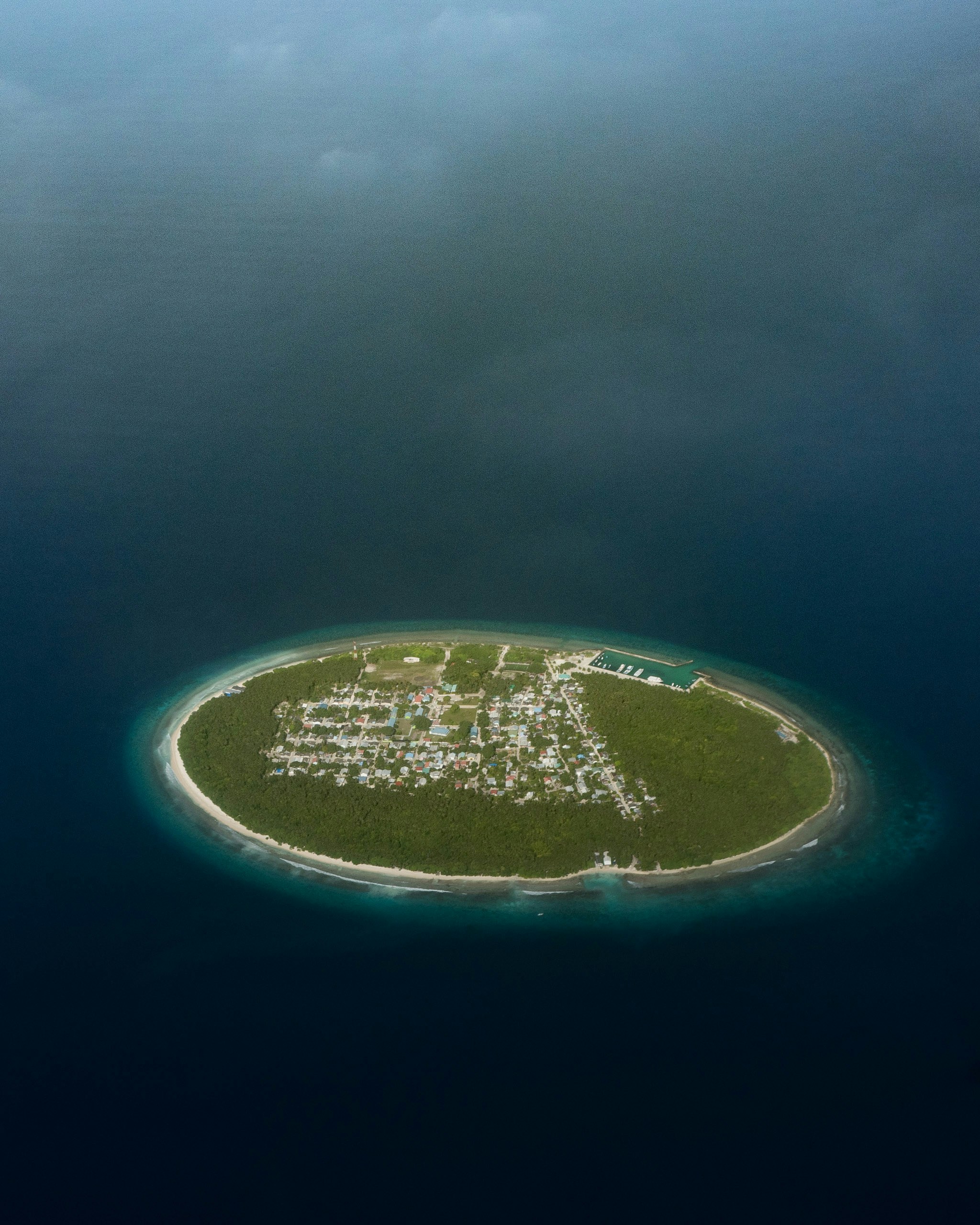 Aerial perspective of a lush, green island surrounded by vibrant blue waters, showcasing a small community and its coastal features.