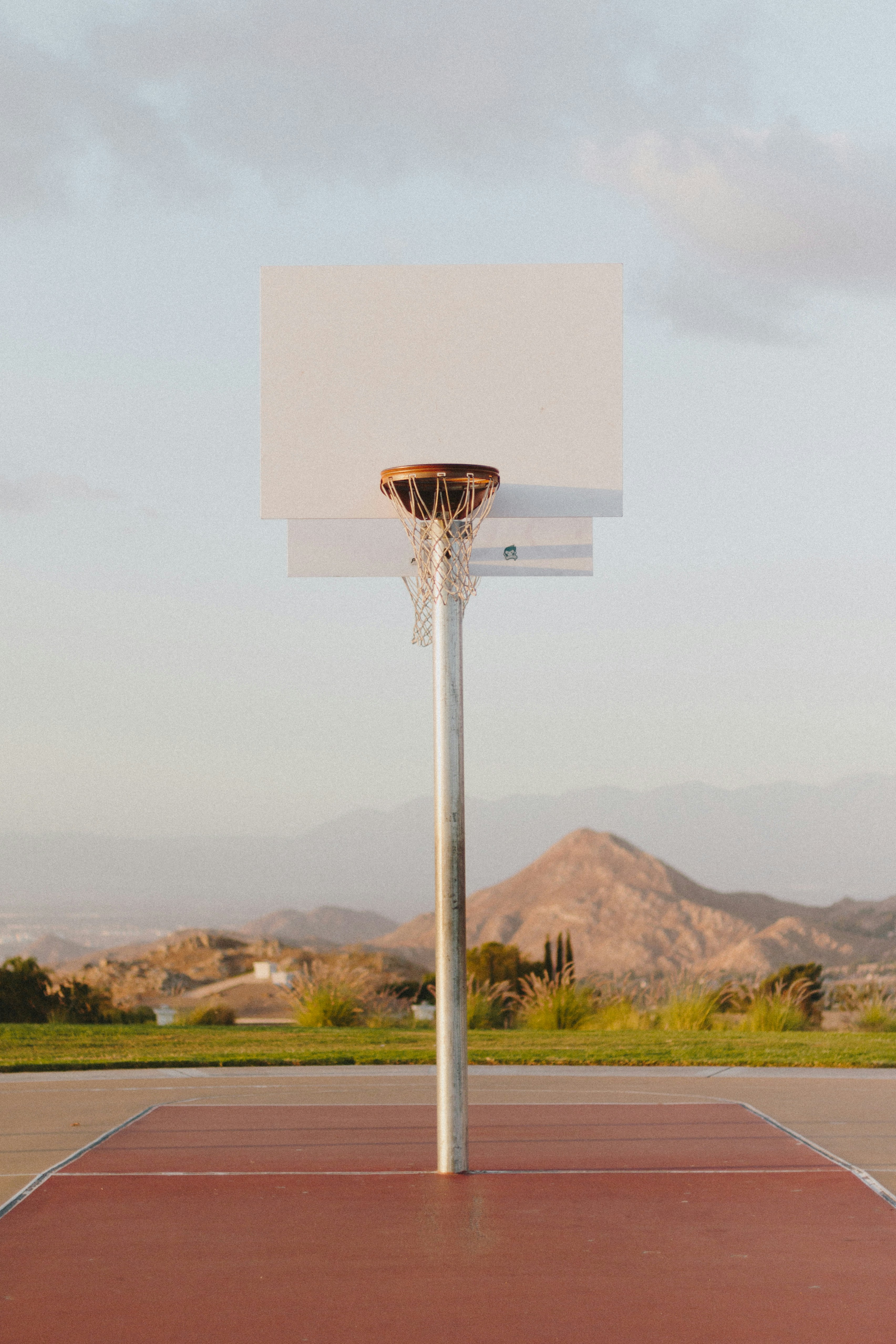 Empty basketball hoop standing alone against a backdrop of rolling hills and a cloudy sky.