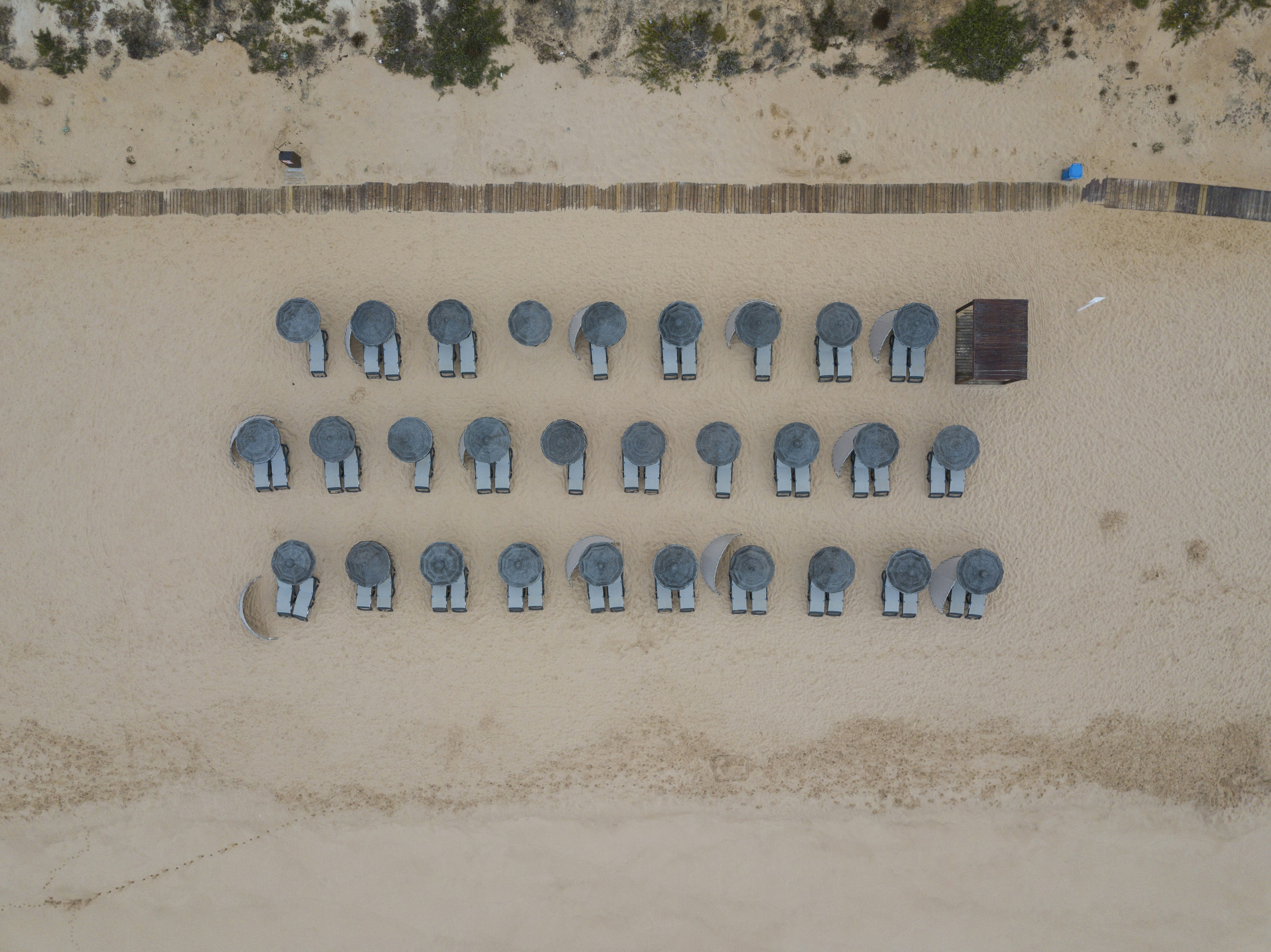 Neatly arranged sun loungers on a sandy beach viewed from above.
