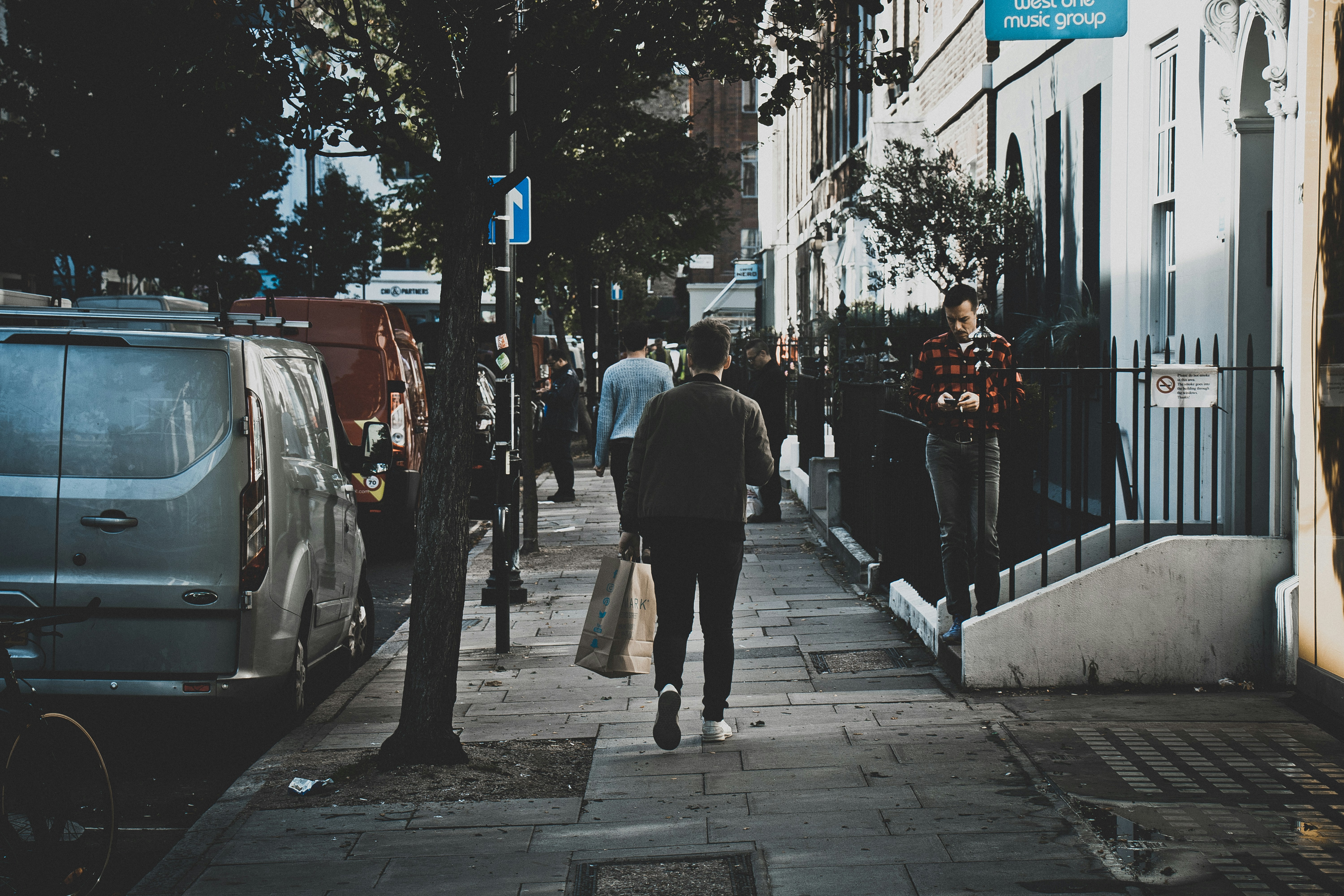 Man walking on street beside buildings while holding paper bag photo ...