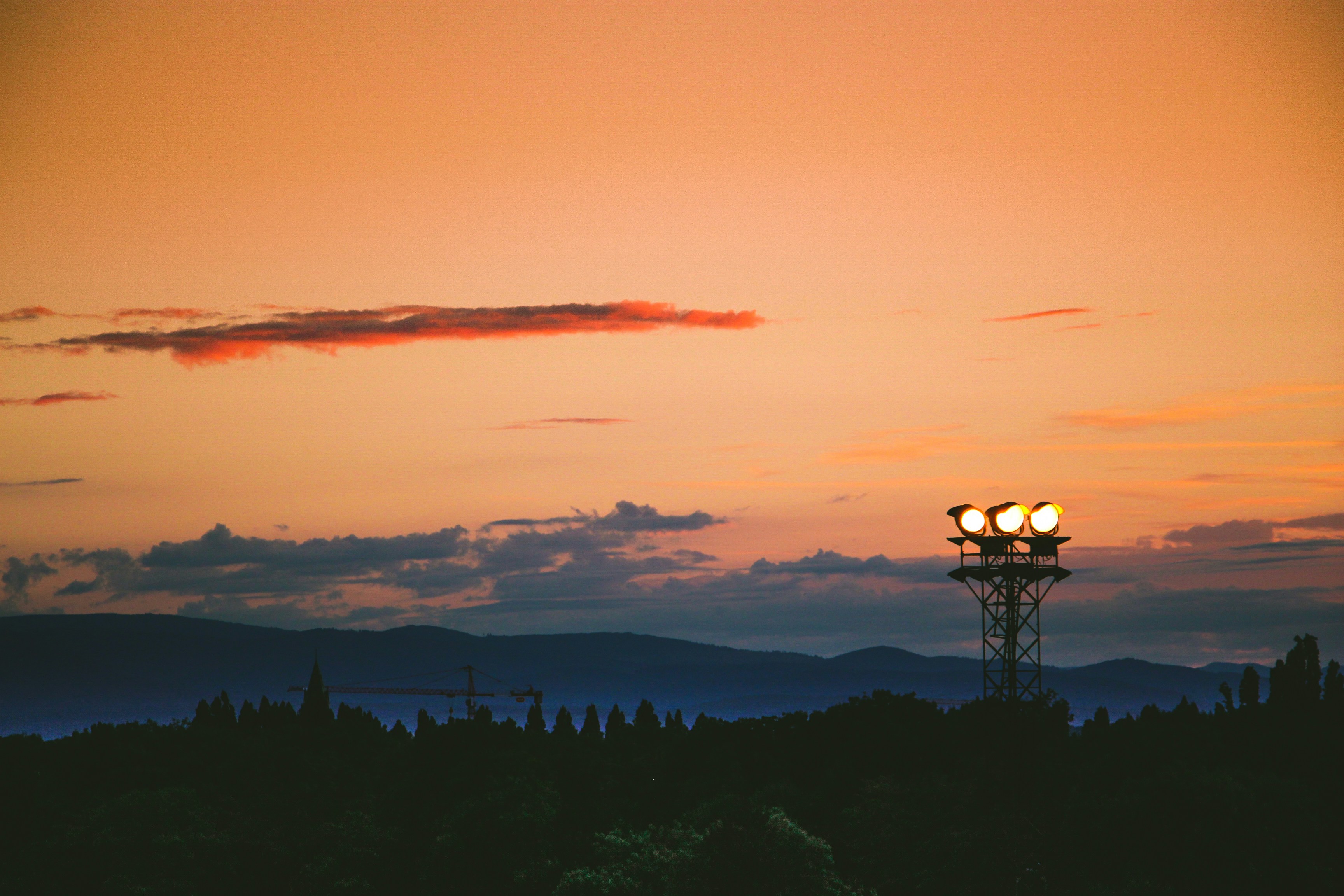 A tall tower with bright lights stands silhouetted against a vibrant sunset sky, casting a serene atmosphere over the landscape.