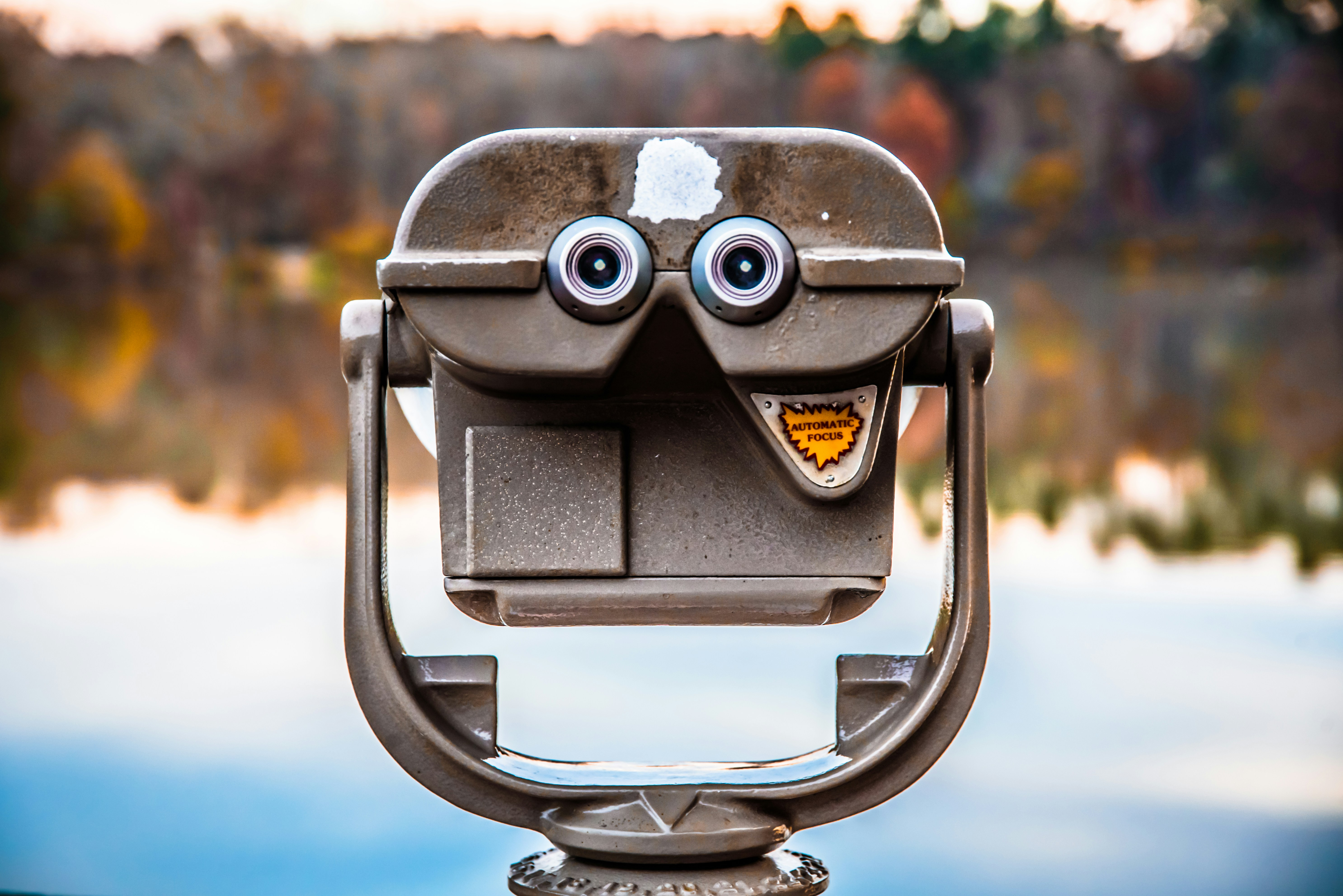 Vintage binocular viewer overlooking a tranquil lake during autumn, reflecting warm hues of the surrounding foliage.