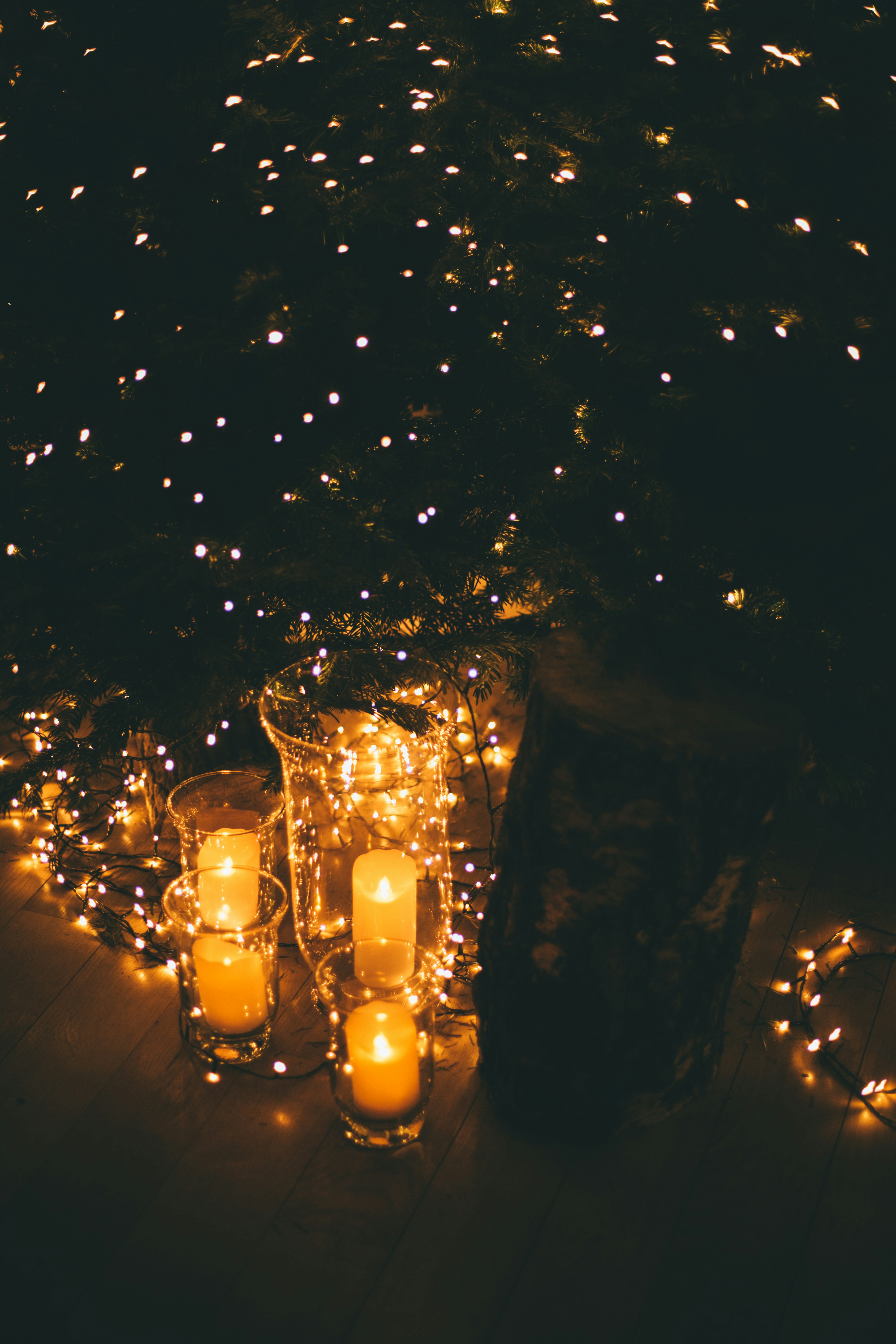 Warm candles glowing softly amidst twinkling lights under a Christmas tree, creating a tranquil holiday atmosphere.