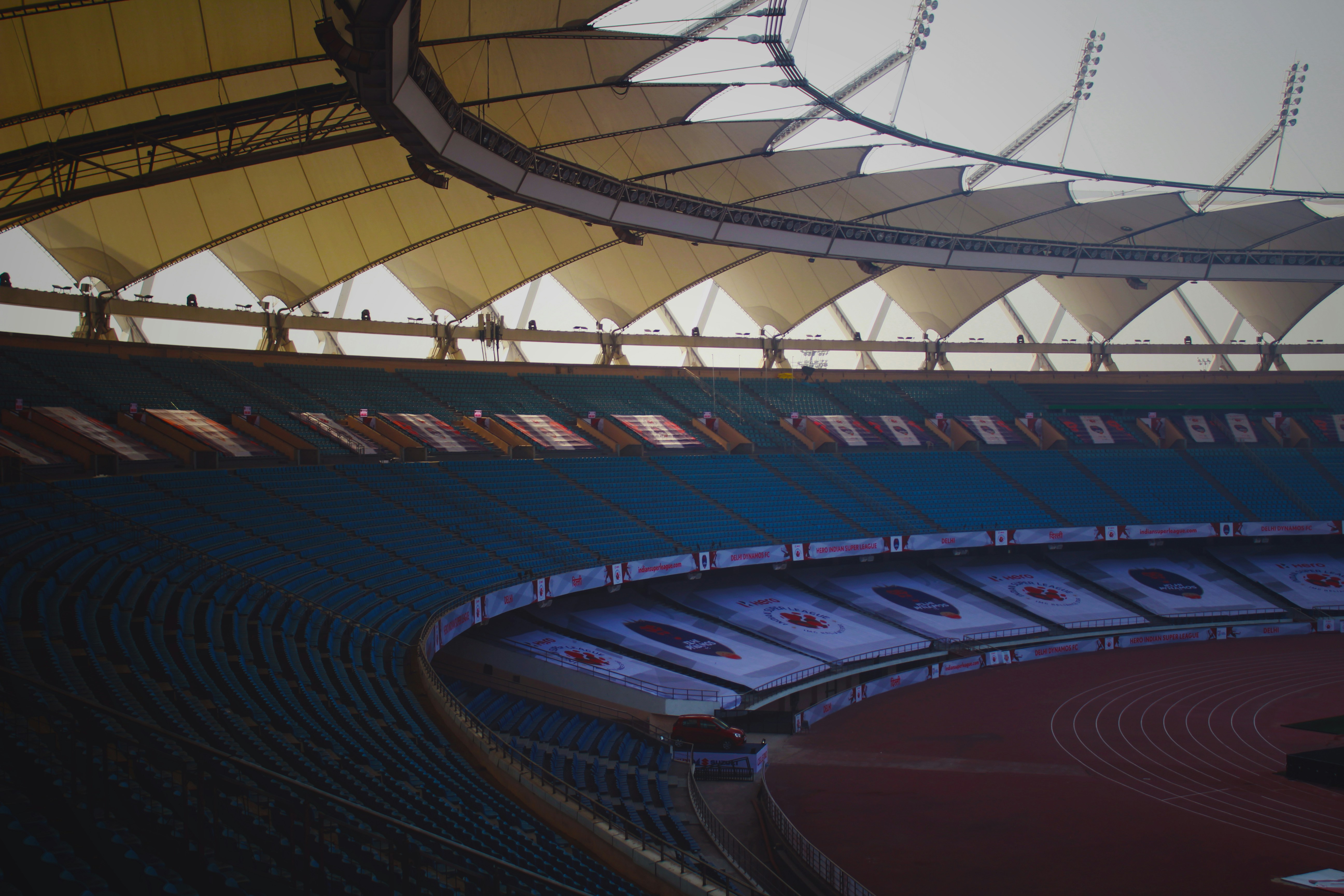 Empty stadium seats under a geometric canopy with a view of the running track.