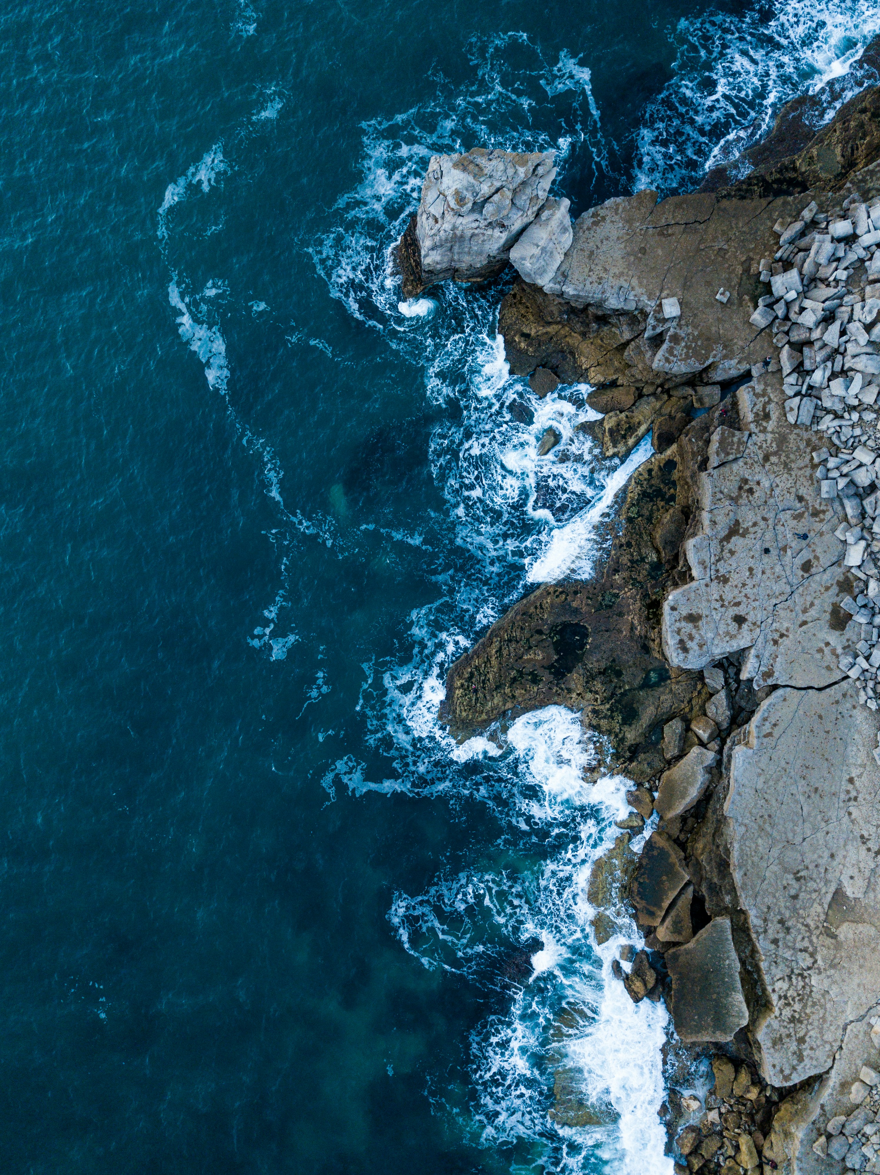 Aerial view of rugged coastline where waves crash against rocky formations, showcasing the dynamic interplay between land and water.