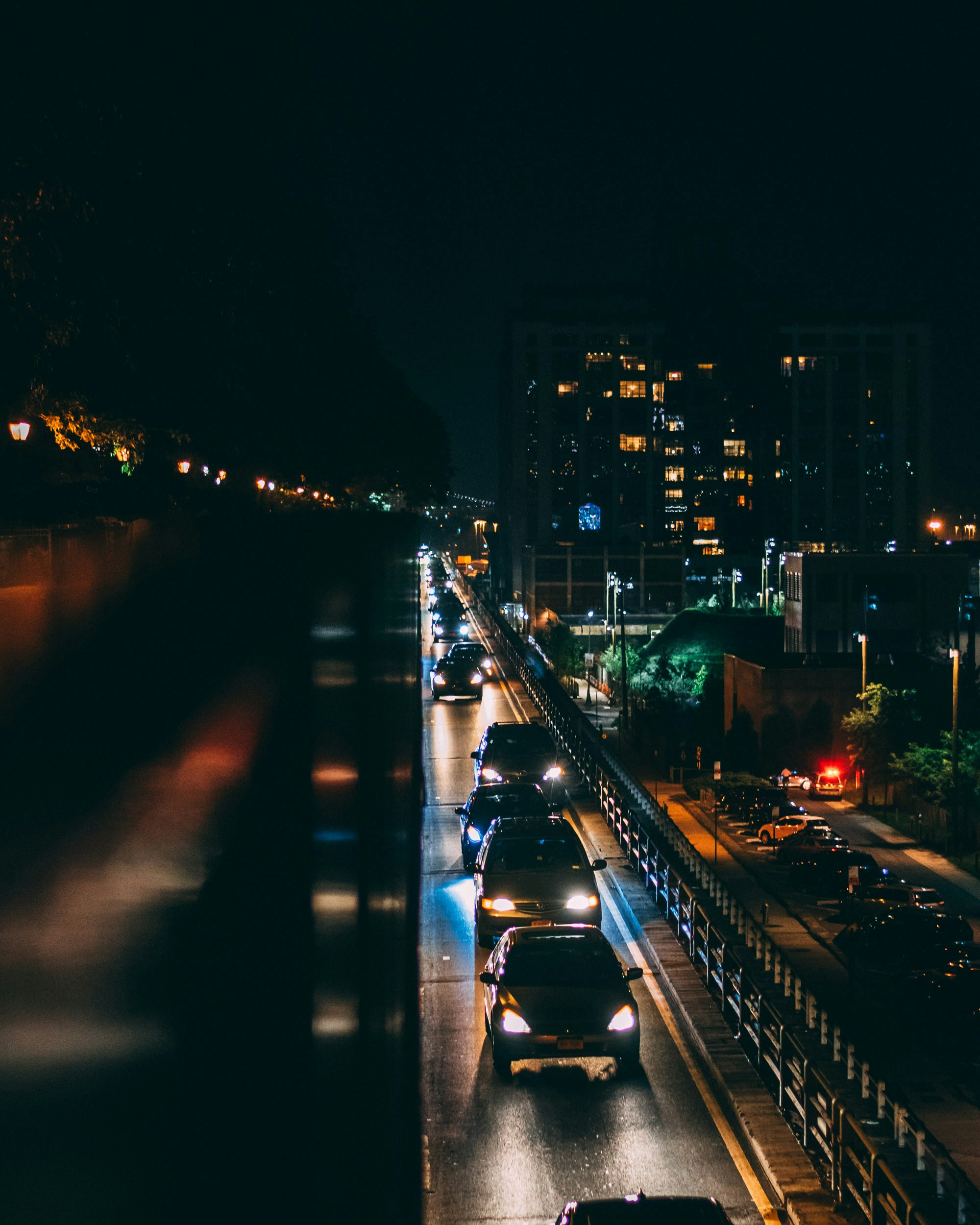 Busy city street illuminated by headlights and streetlights, showcasing the flow of traffic at night with buildings in the background.