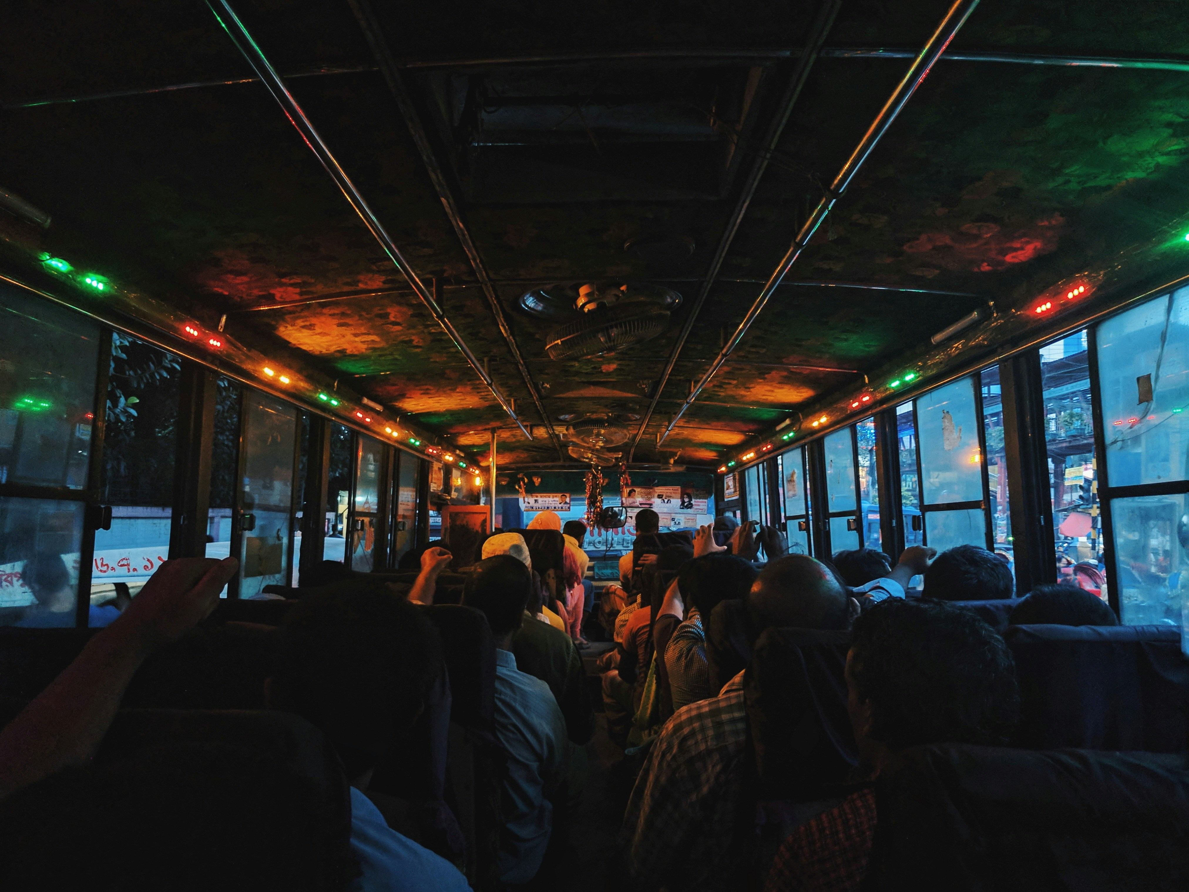 Interior of a crowded bus illuminated by colorful lights, showcasing passengers in a lively urban setting.