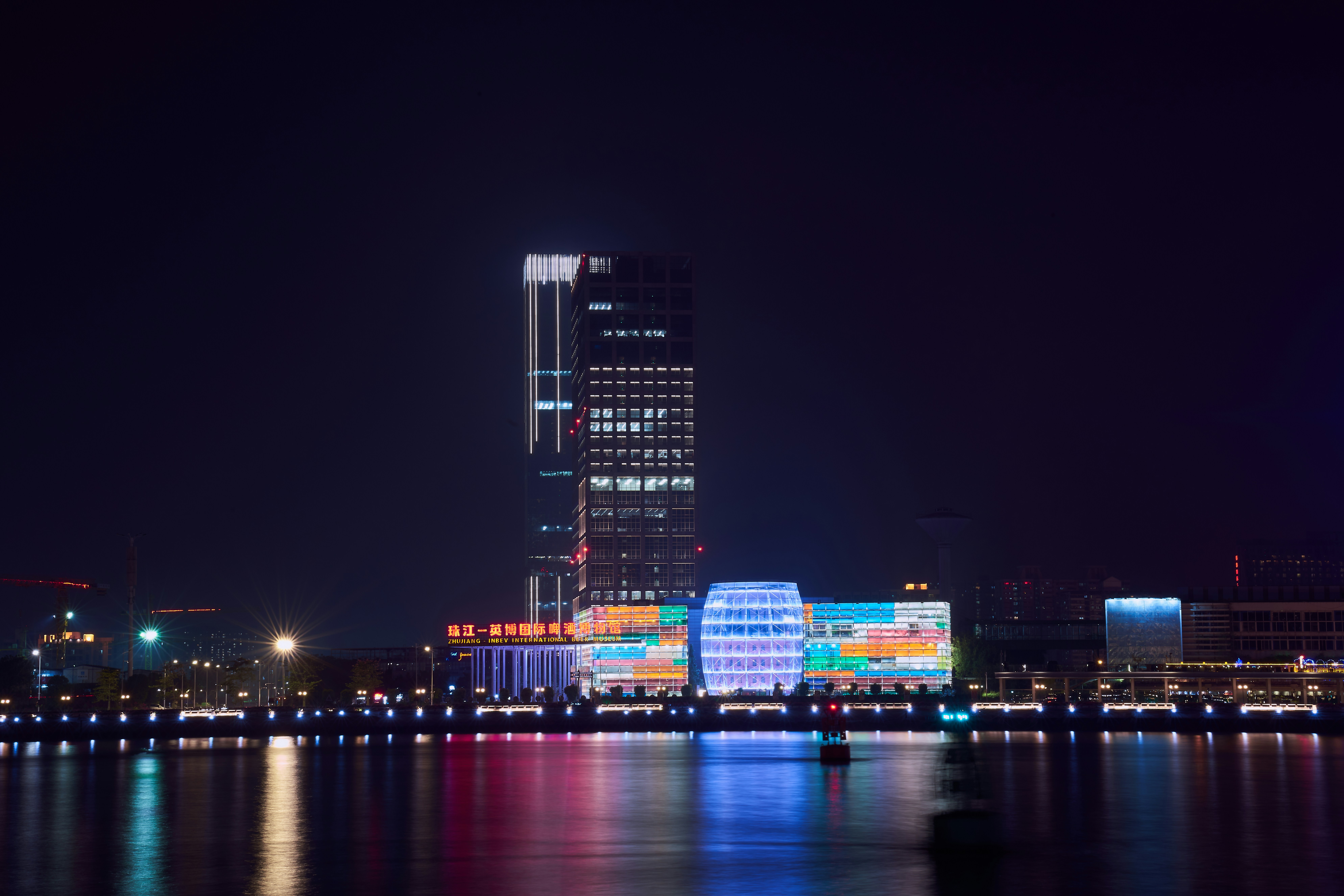 Illuminated skyscraper and buildings reflected in a calm waterfront at night.
