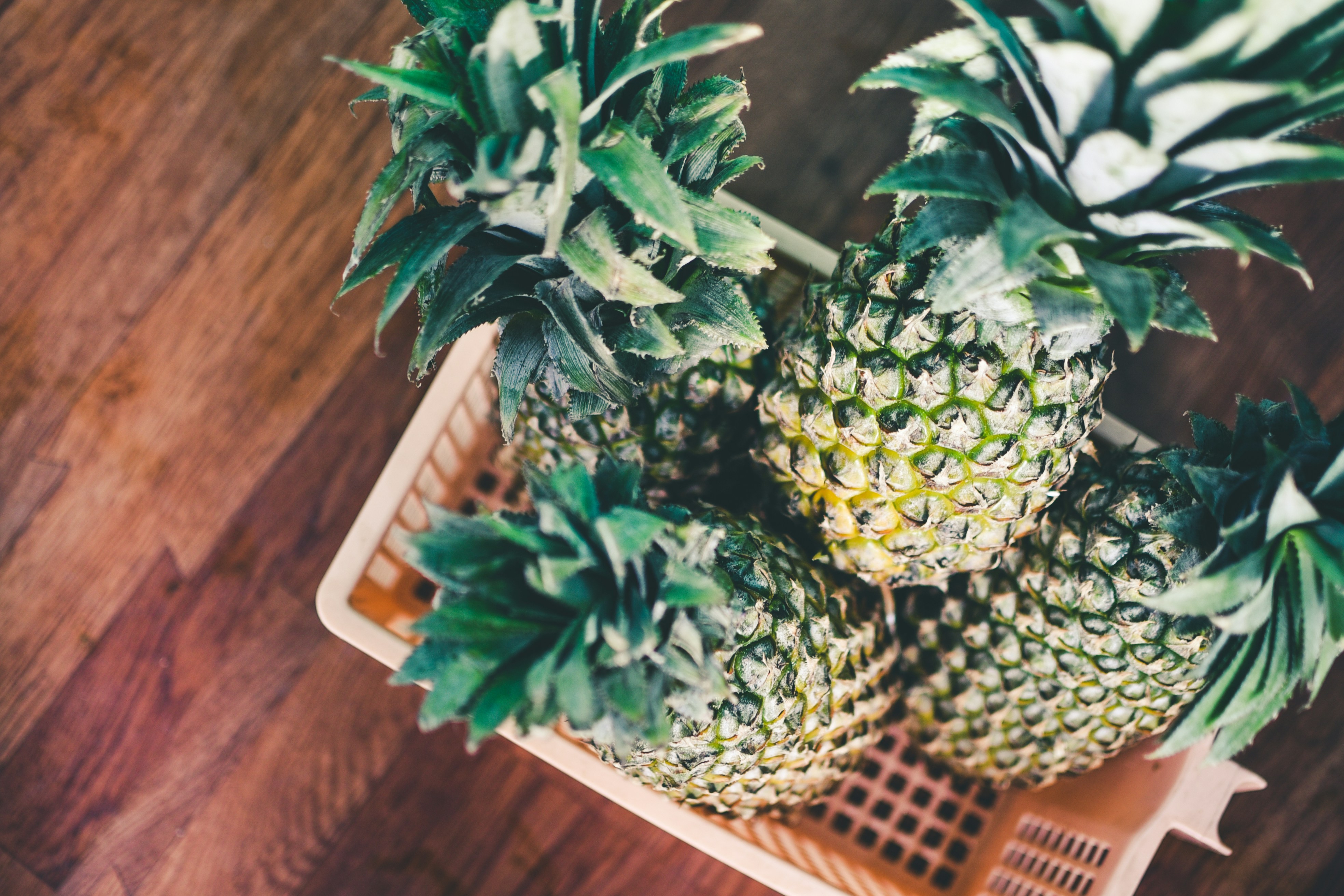 Fresh pineapples arranged in a light-colored basket on a wooden surface, showcasing their vibrant green leaves and textured skin.