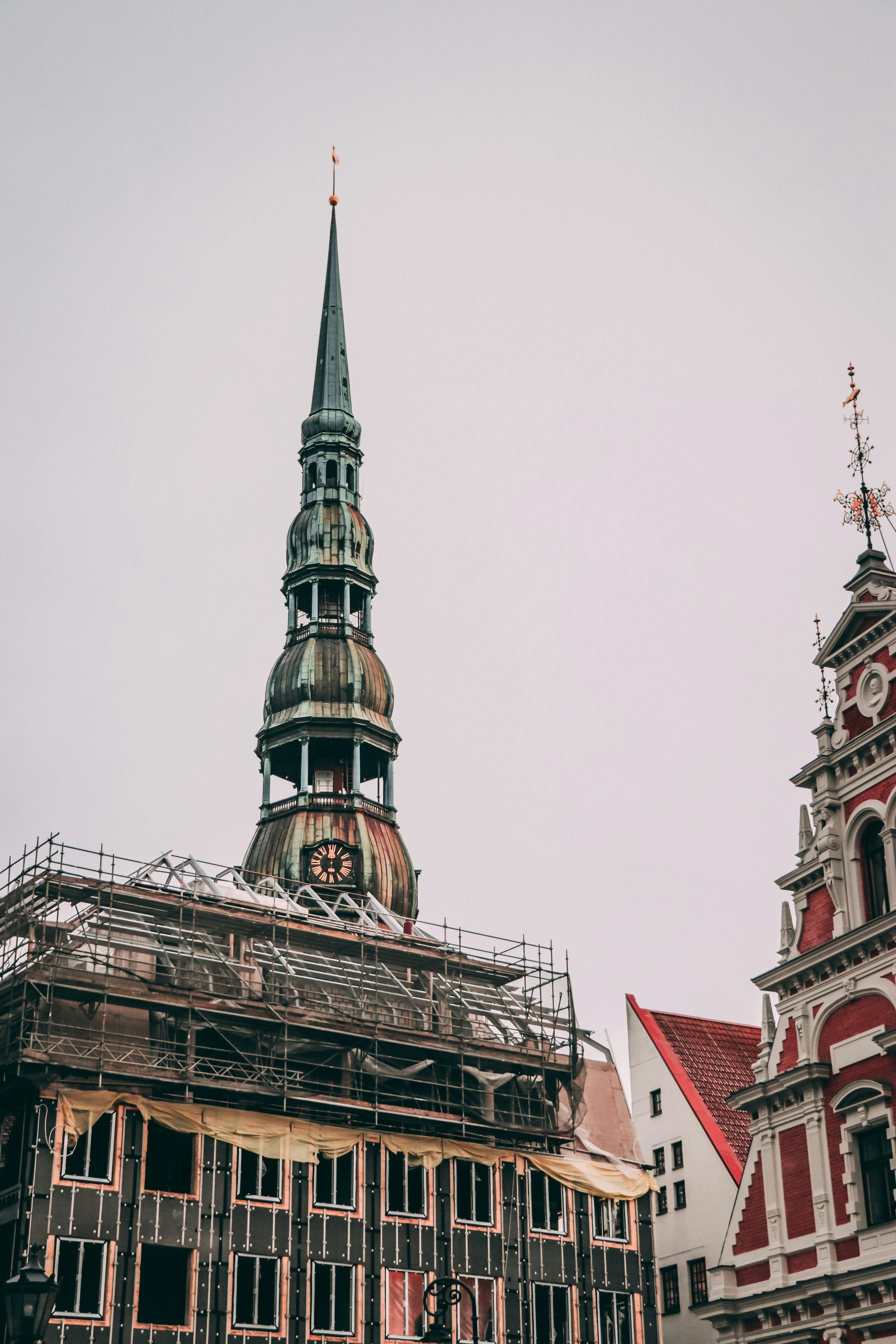 The spire of a historic church stands tall amidst renovation scaffolding, showcasing intricate architectural details against a muted sky.