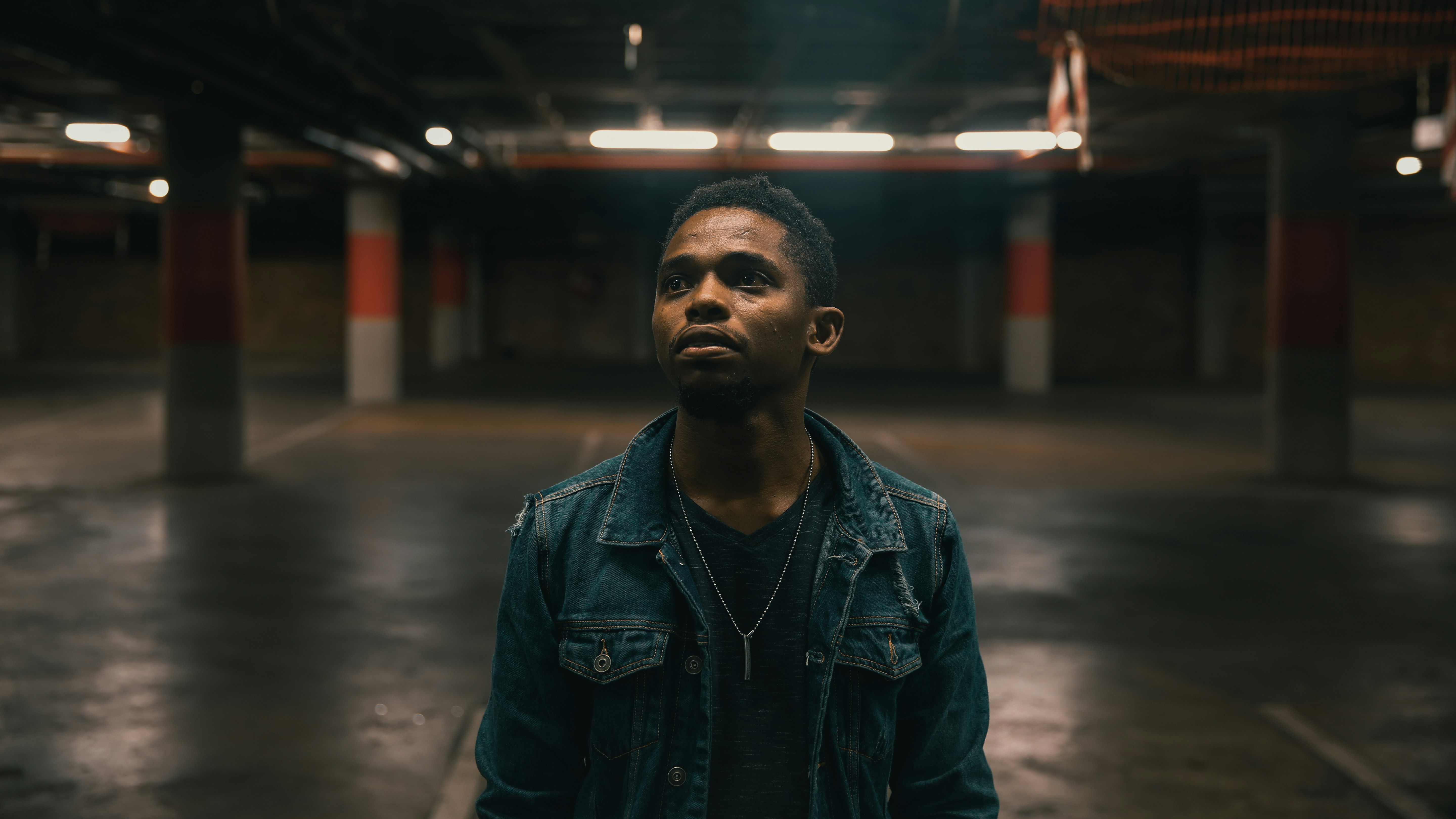 Young man gazing upward in an empty underground parking garage, illuminated by soft overhead lighting.