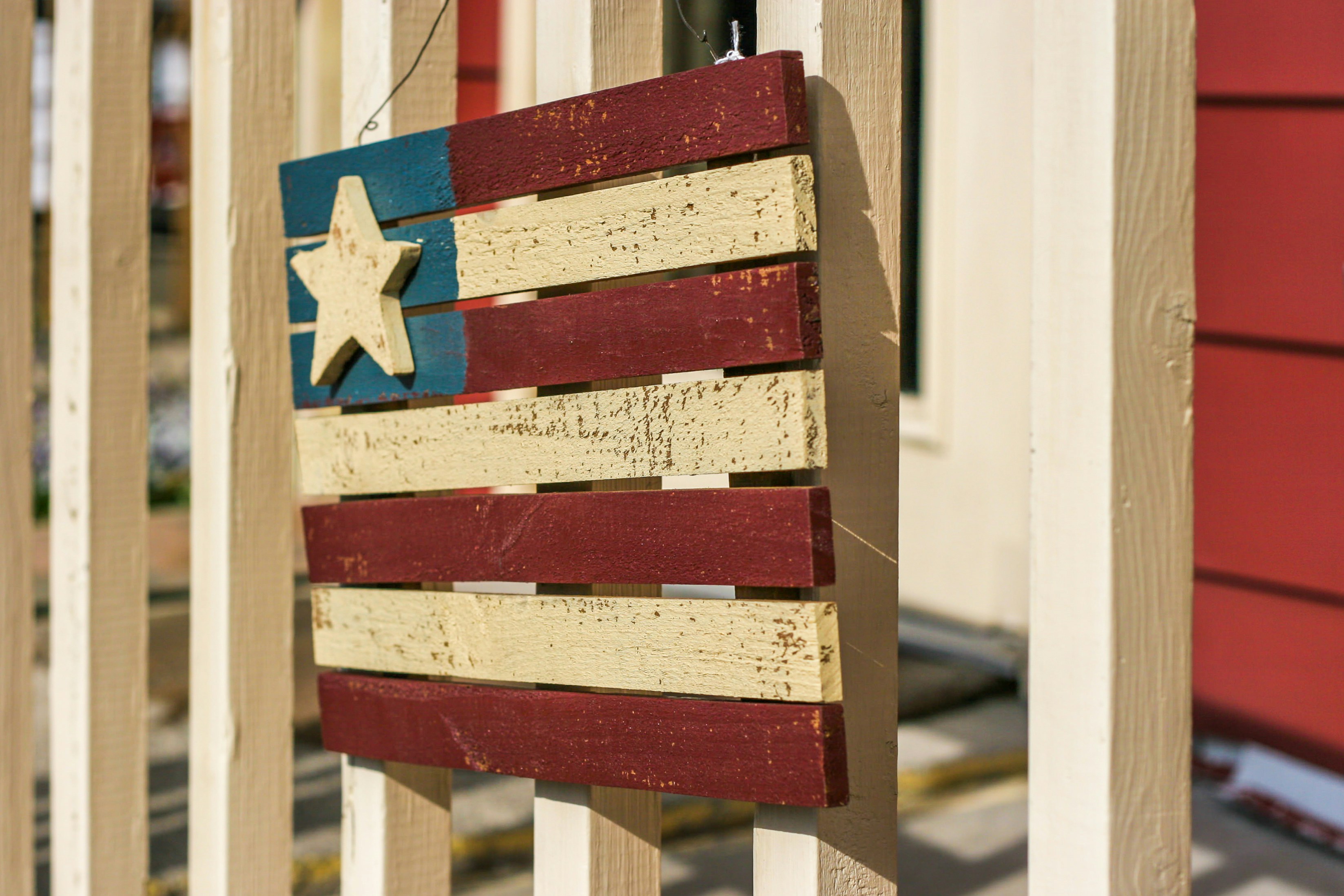 Handcrafted wooden flag with a star, featuring red, white, and blue colors, displayed against a wooden fence.