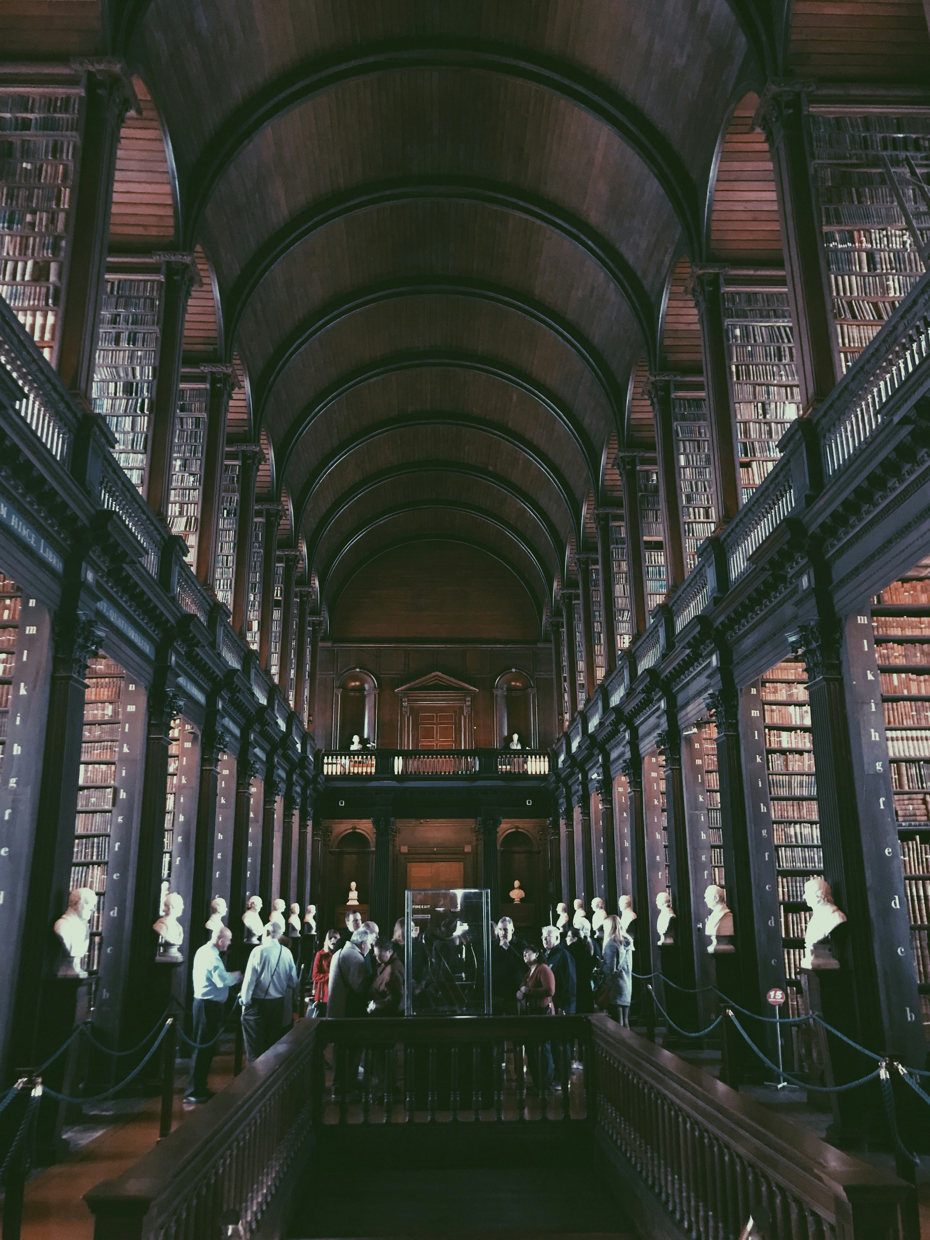 Interior view of a historic library featuring towering bookshelves and classical busts, with visitors exploring the space.