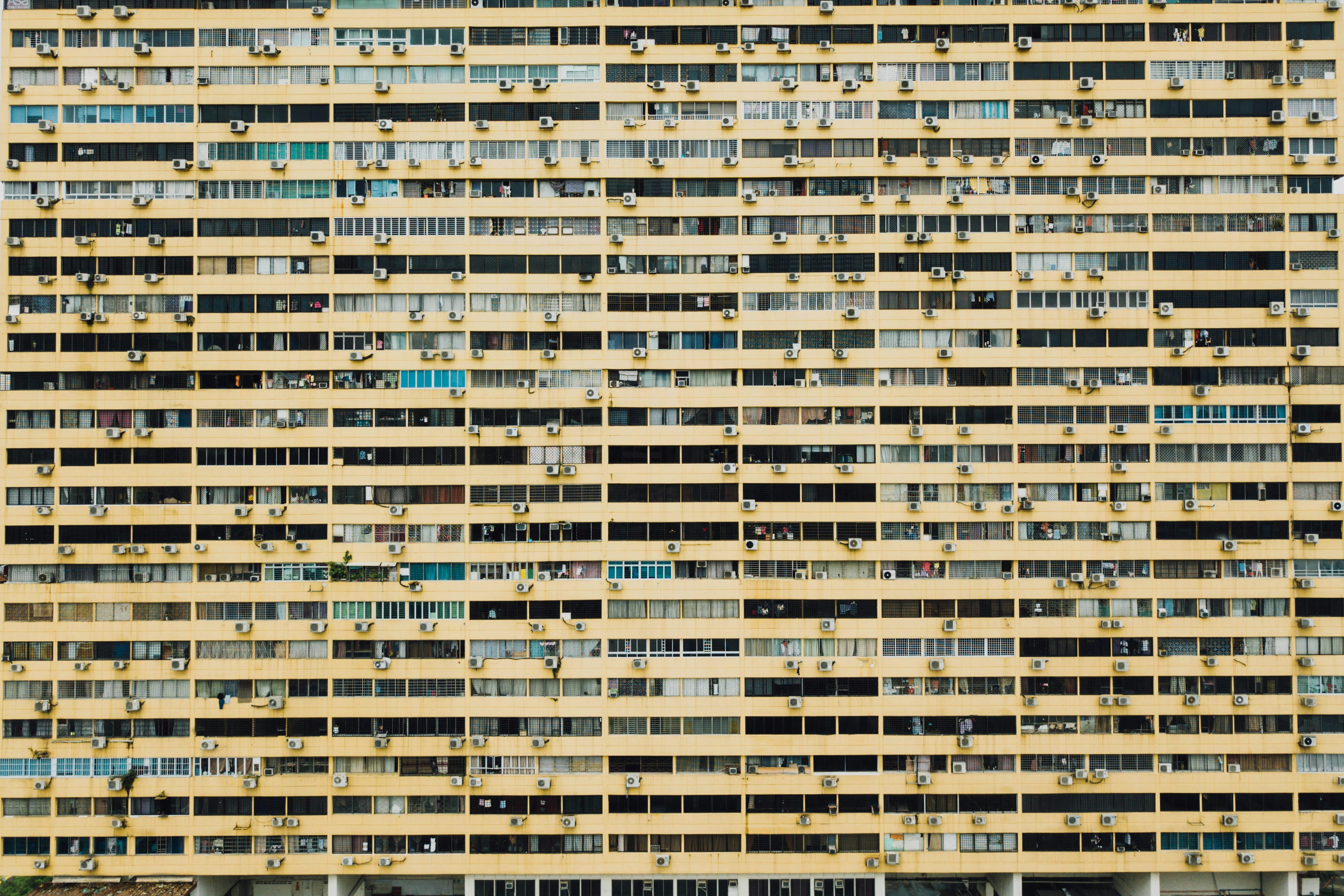 Facade of a high-rise building showcasing a grid of balconies and air conditioning units, reflecting urban life and architectural design.