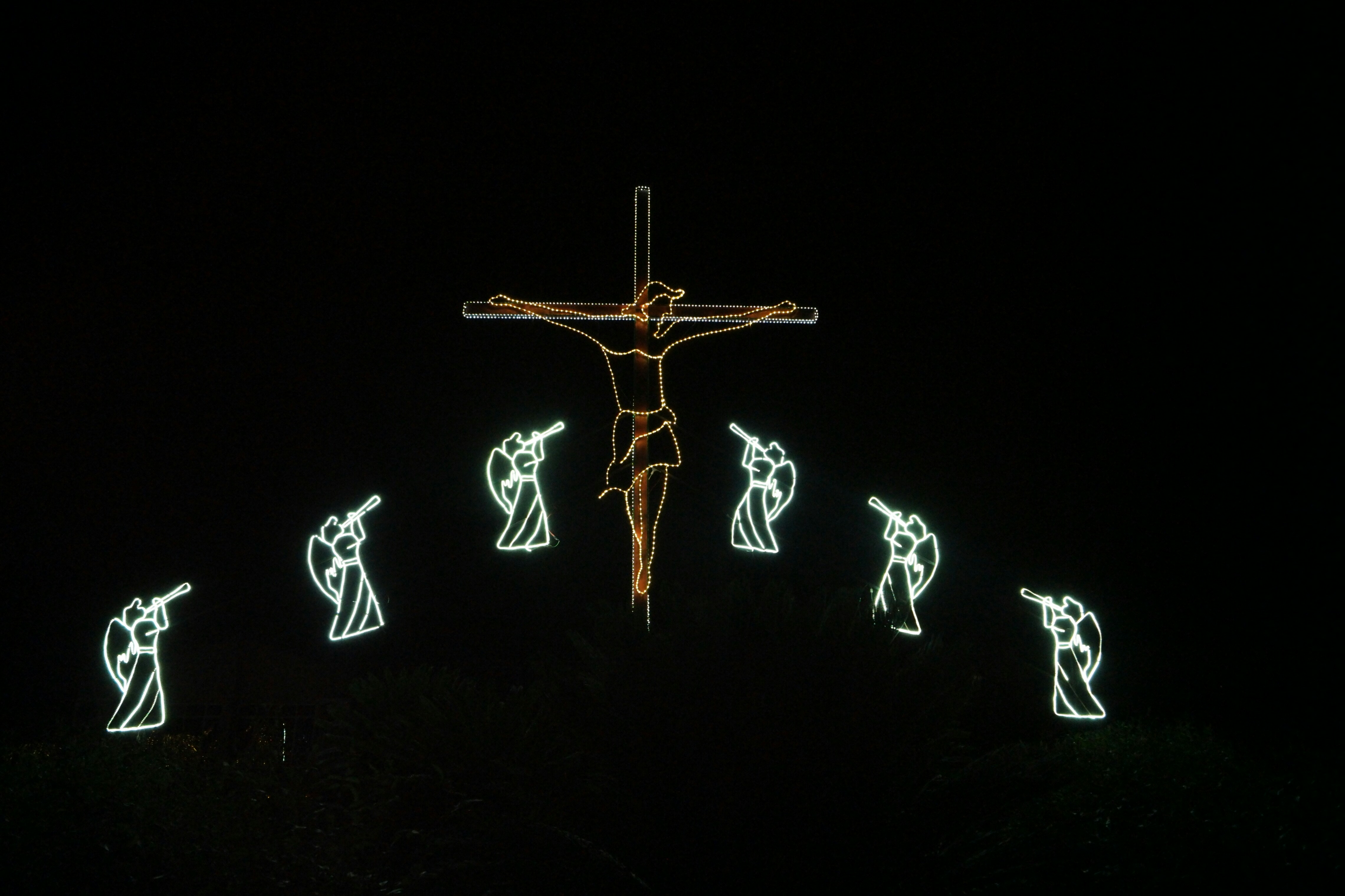 Crucifix surrounded by glowing angel figures in a dark setting.