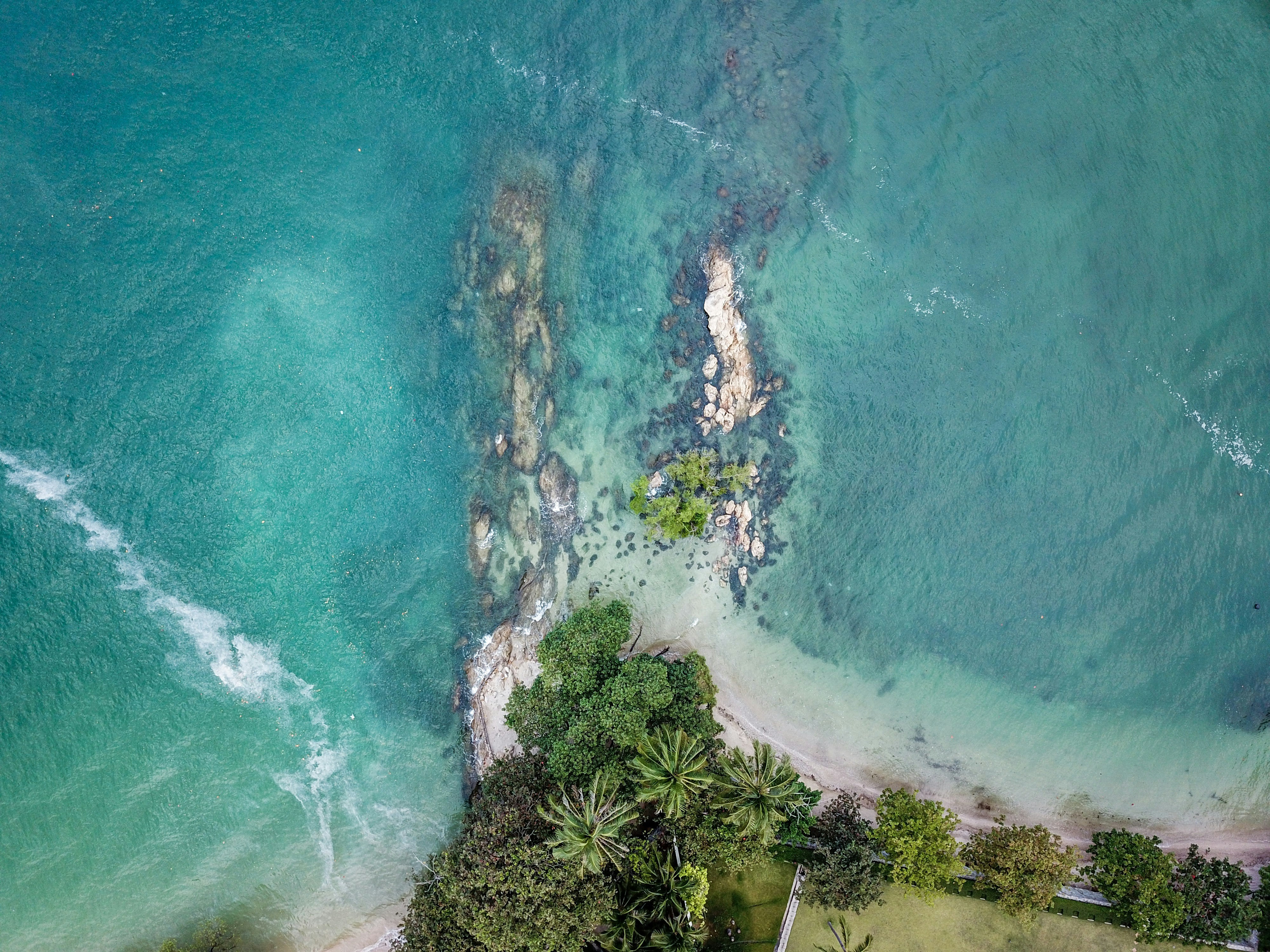 Aerial view of a vibrant coastline featuring rocky outcrops and lush greenery alongside azure waters. The scene captures the harmony between land and sea.