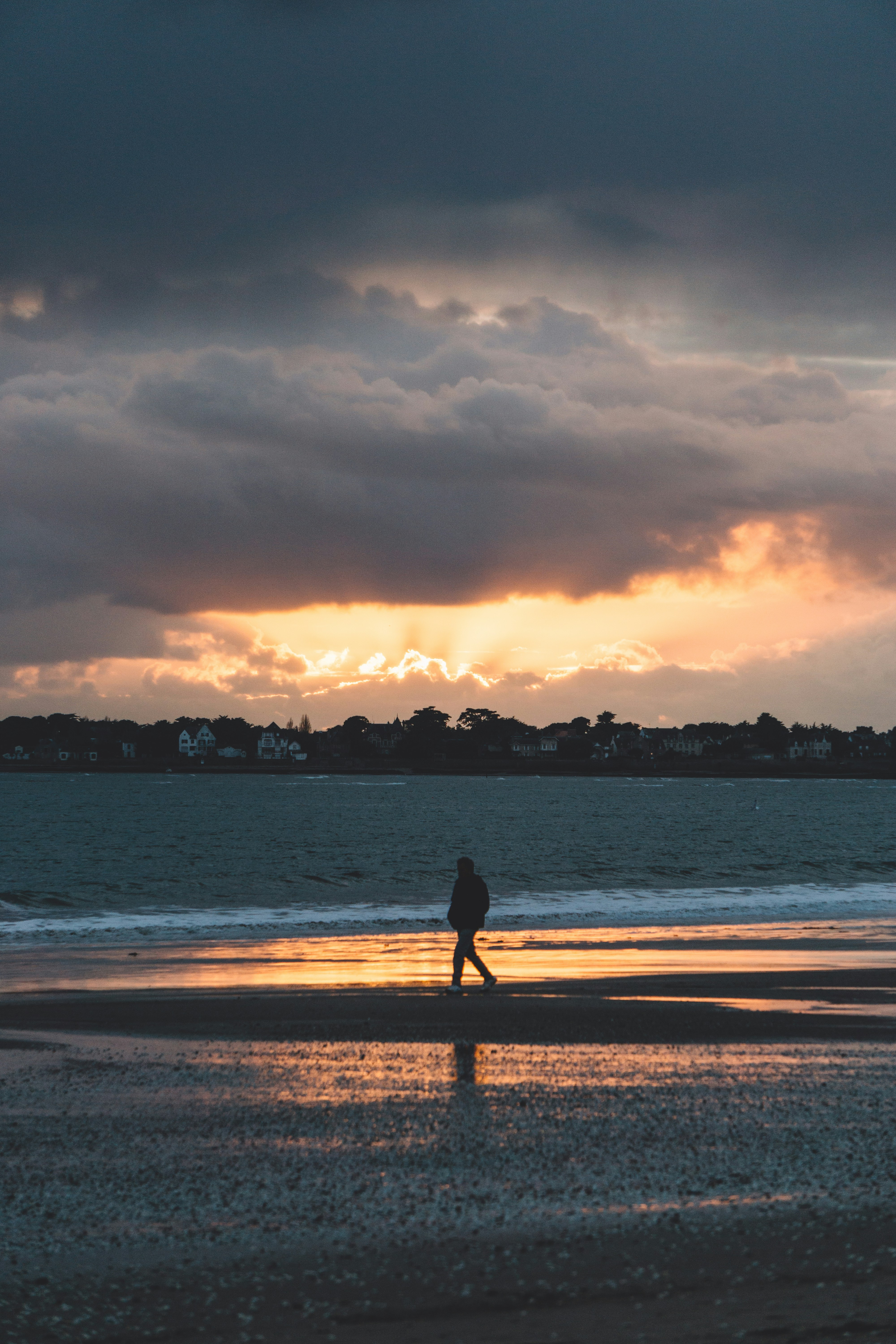 Ember Dusk: A lone silhouette treads the shoreline beneath dramatic clouds