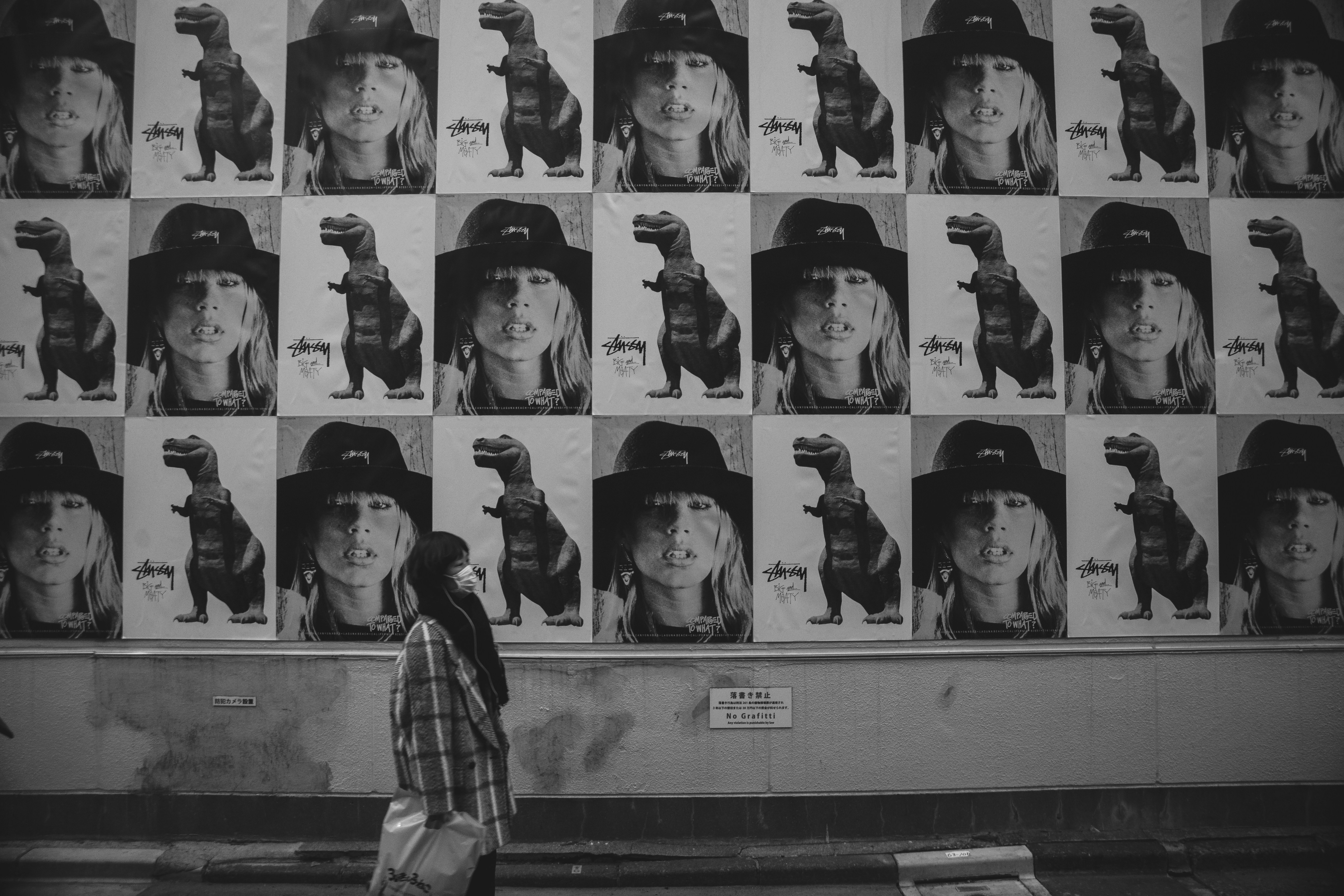 Grayscale wall art featuring repeated images of a person in a hat and a dinosaur, with a passerby in motion.