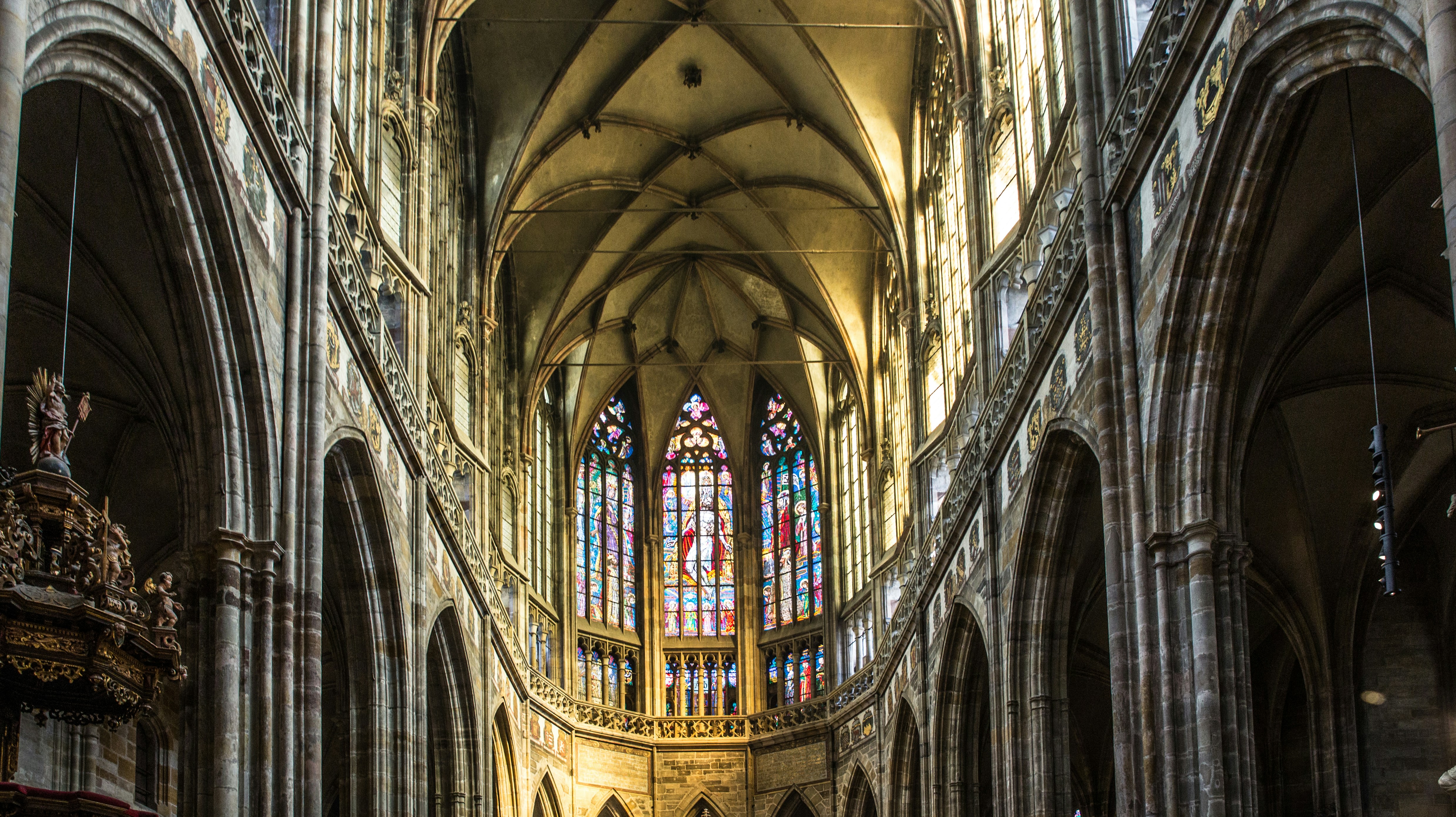Gothic cathedral interior showcasing intricate arches and vibrant stained glass windows. Light filters through, enhancing the architectural details.