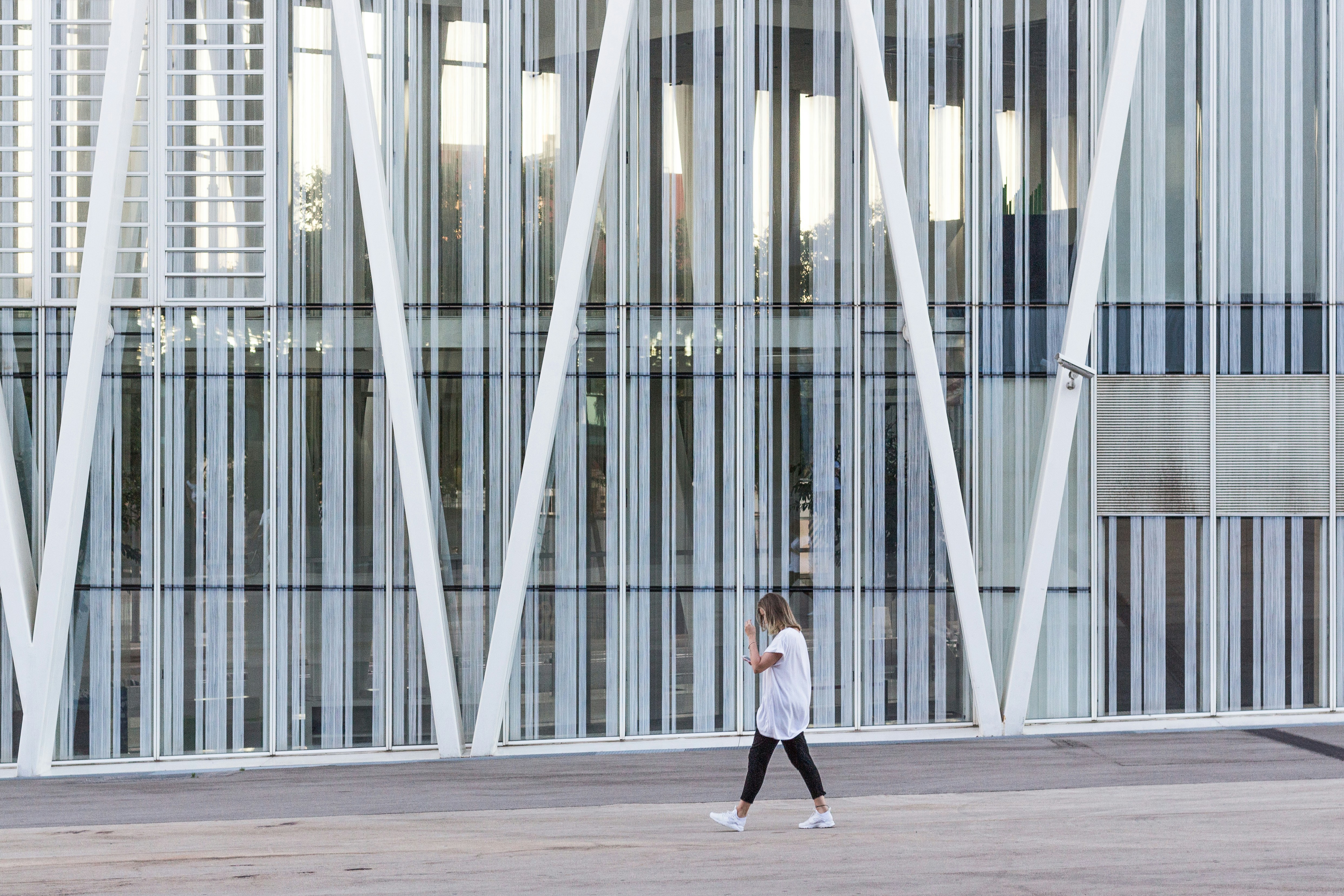 Stride Under the Glass Cathedral: a lone pedestrian against diagonal white supports