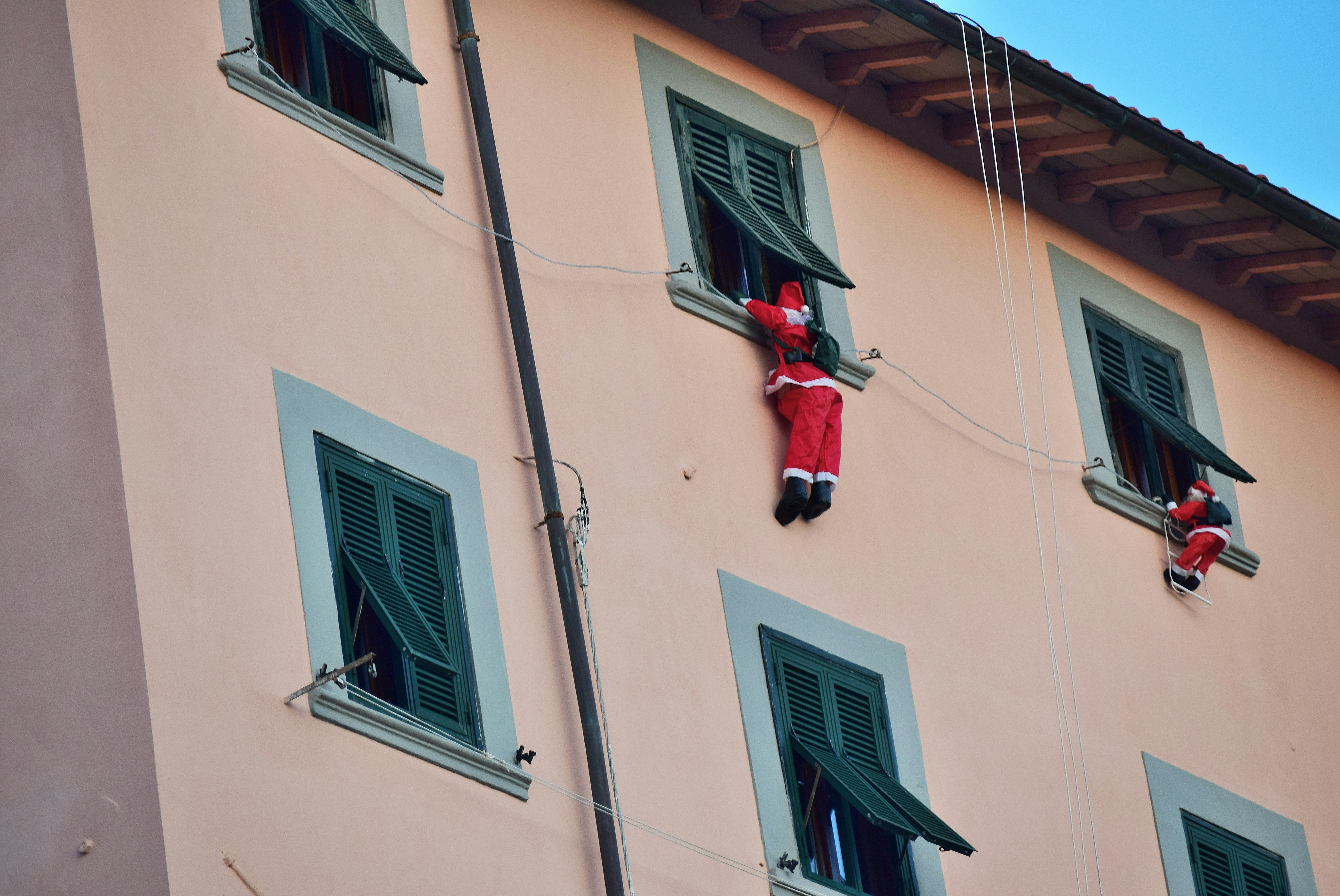 Two Santa figures climbing out of windows on a pastel-colored building, adding a whimsical holiday touch to the scene.