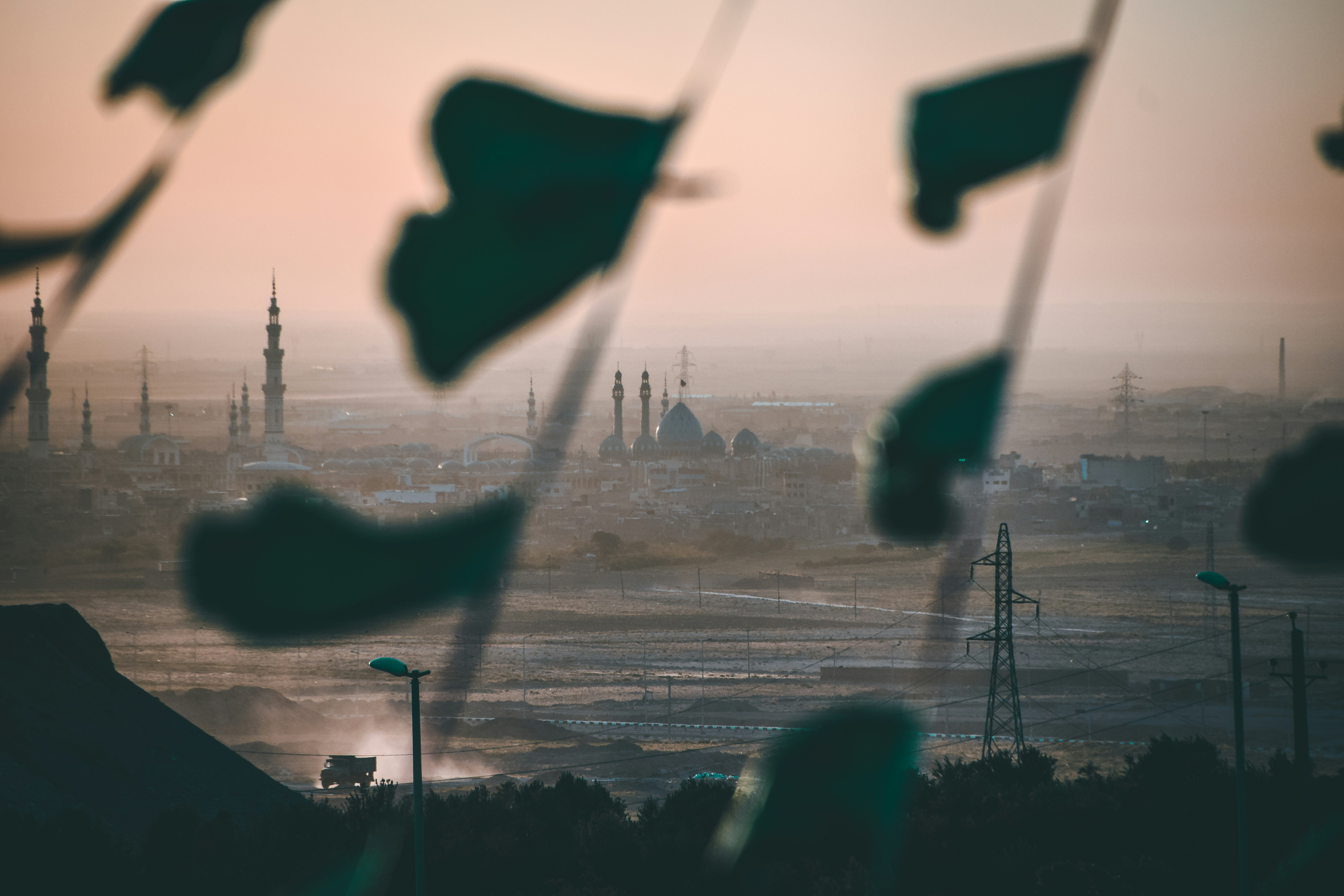 Silhouetted flags and distant minarets create a serene scene at dusk, with warm tones enveloping the landscape.