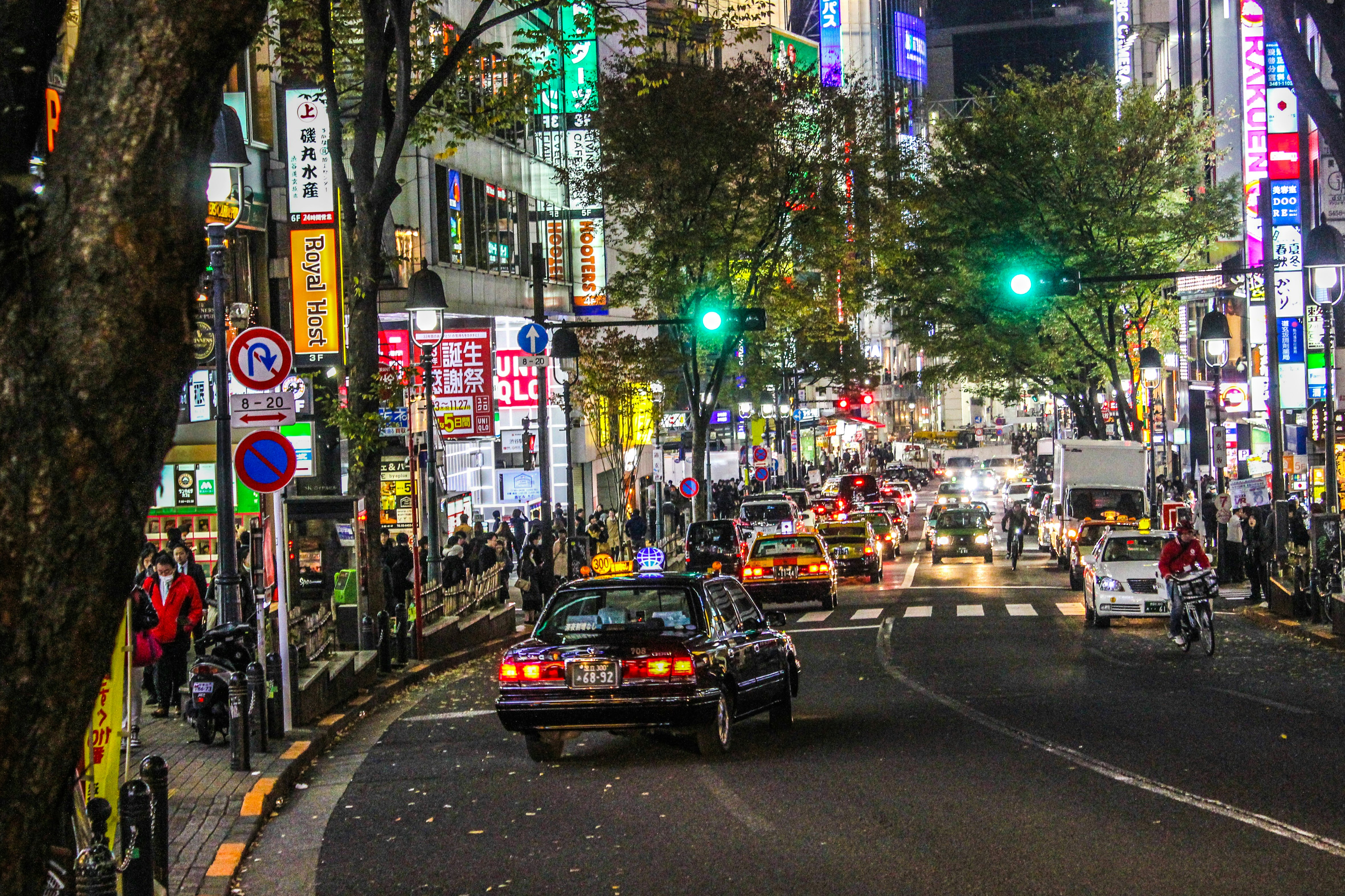 Bustling Shibuya street illuminated by vibrant neon lights and busy traffic under night sky.