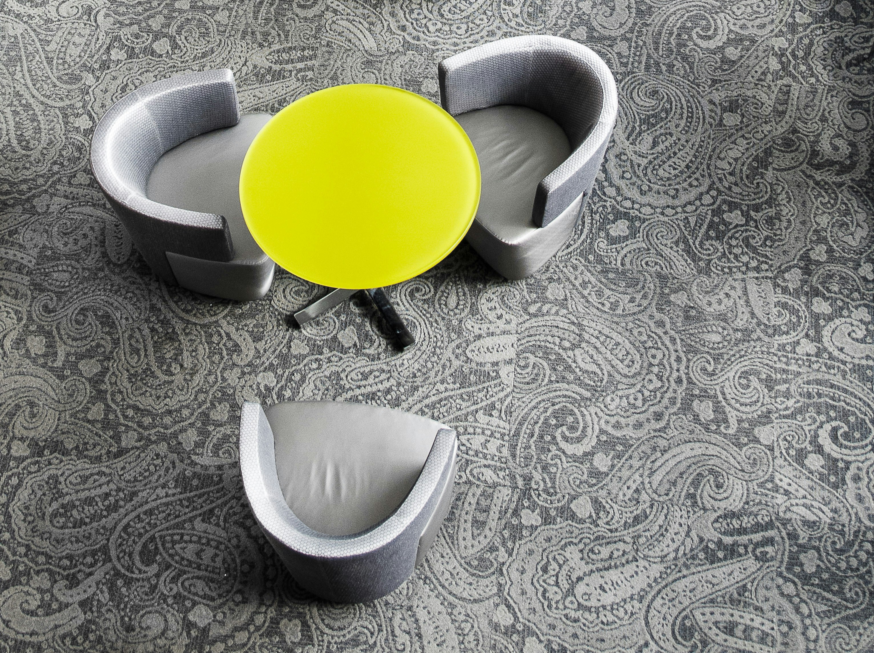 Bright yellow round table surrounded by three gray tub chairs on a patterned carpet.