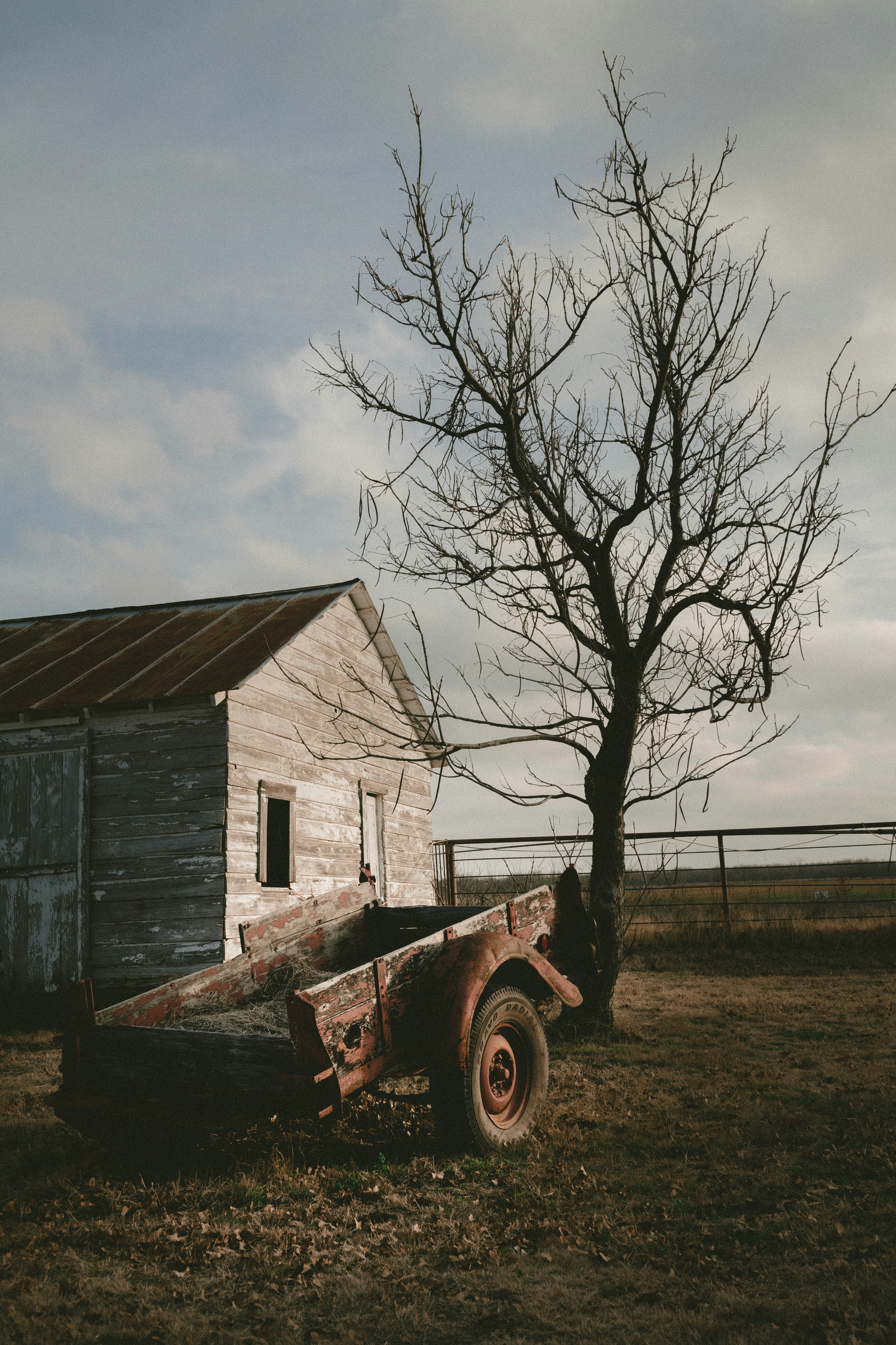 Rusty trailer beside a weathered wooden shed under a cloudy sky, evoking a sense of nostalgia and abandonment.