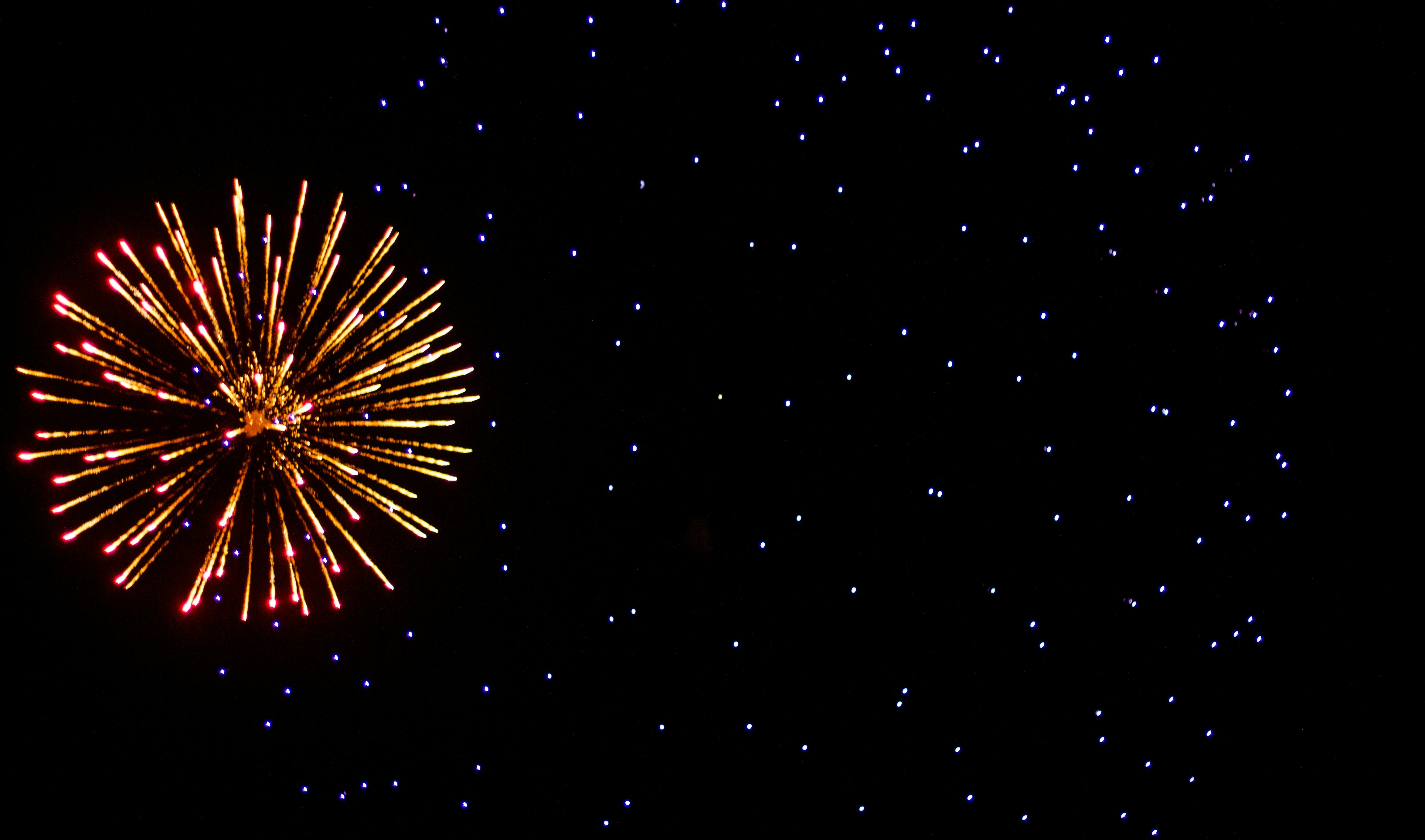 Vibrant firework explosion illuminates the night sky, surrounded by twinkling stars. Colors dance in a dazzling display.